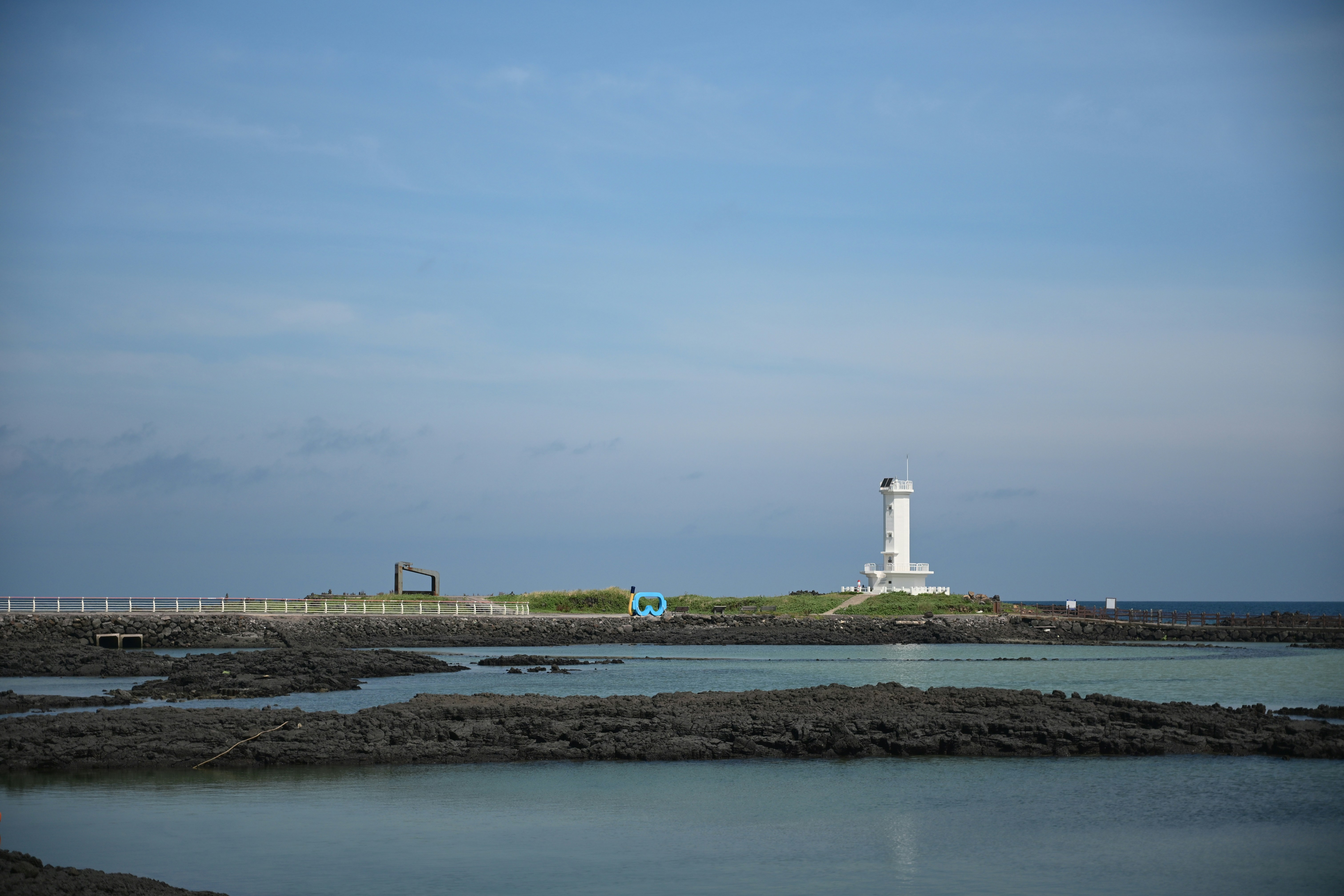 A white lighthouse stands on a rocky shore.
