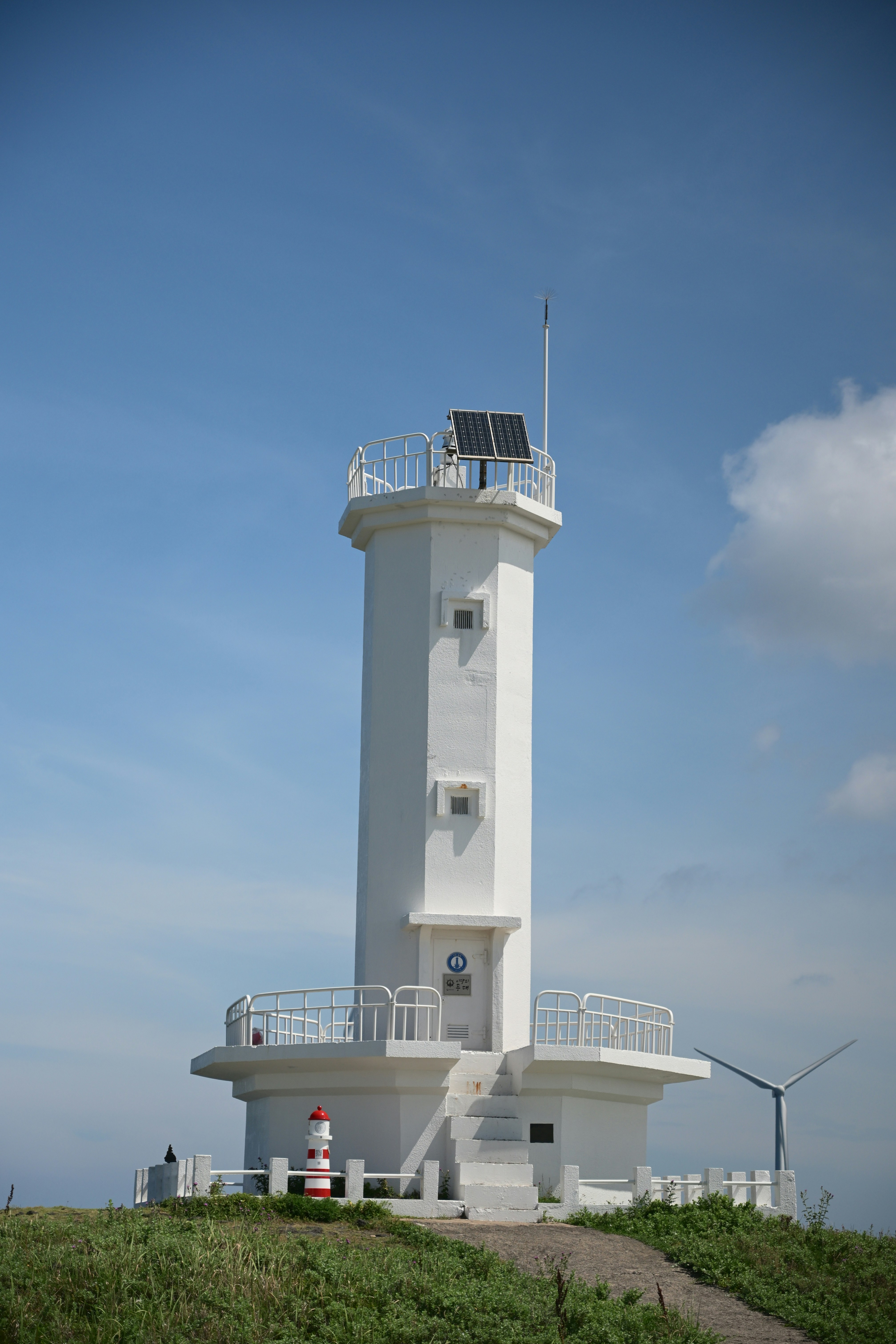 A white lighthouse stands tall against a blue sky.