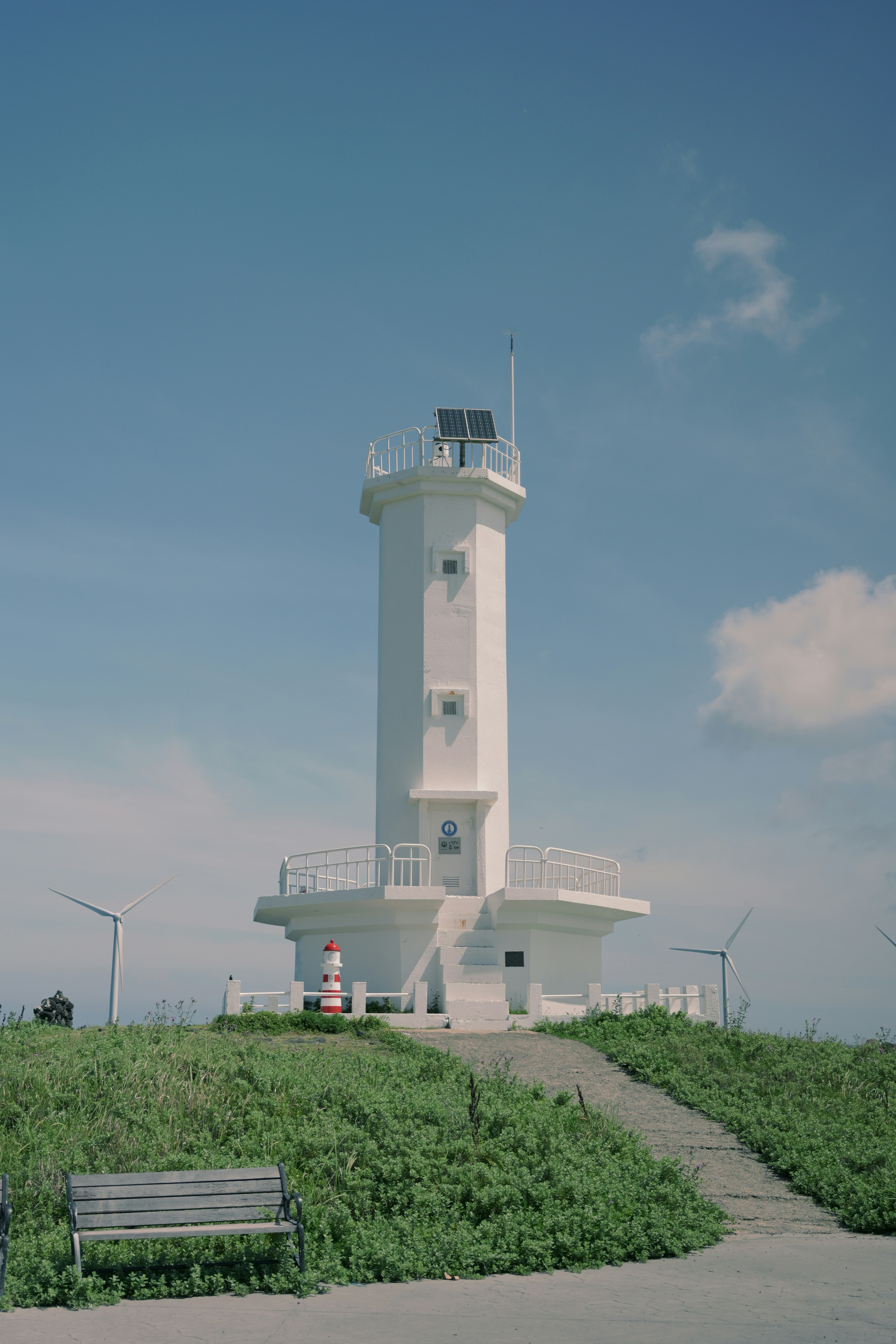 White lighthouse on a grassy hill with windmills.