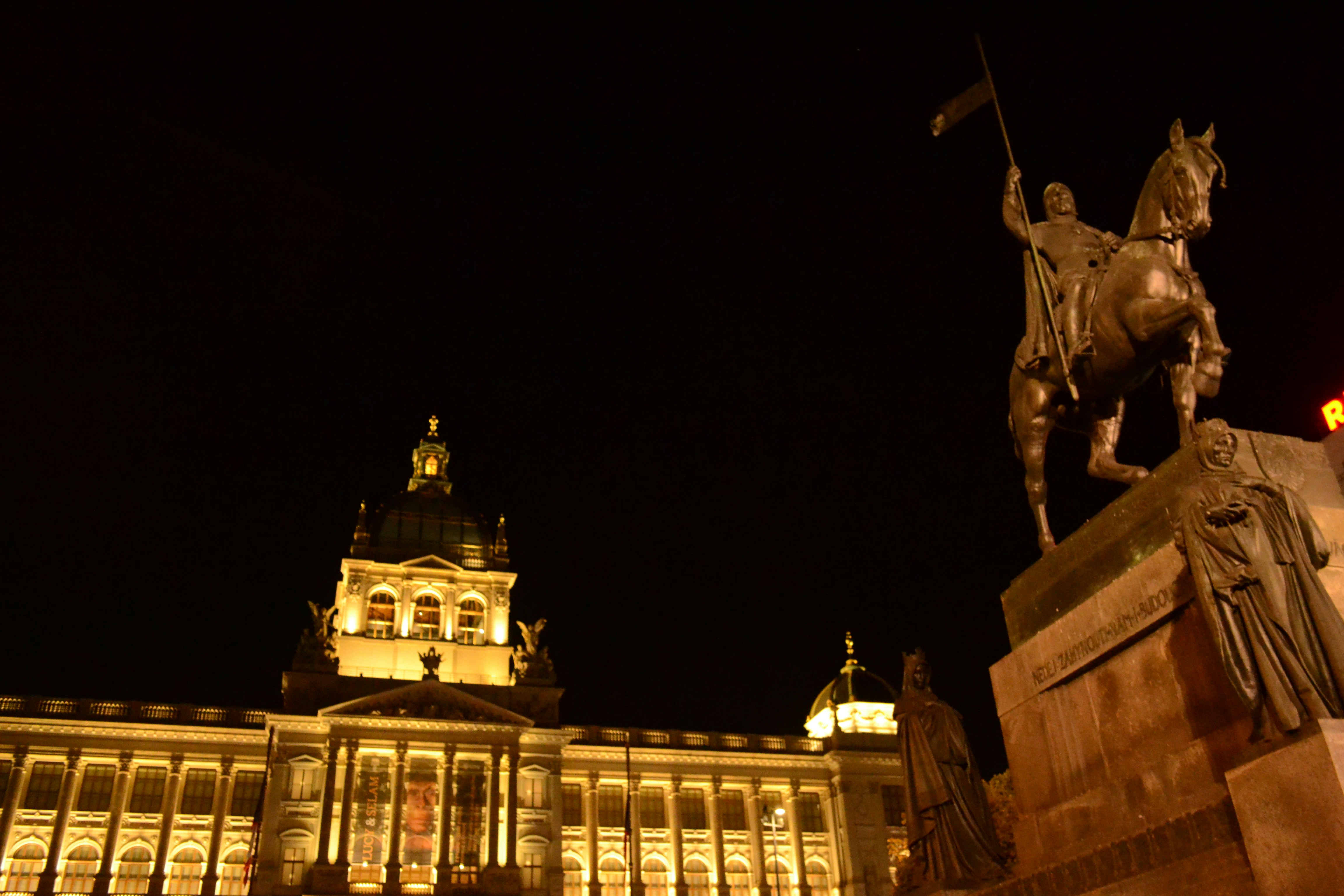 Statue of a knight on horseback in front of a grand illuminated building at night.