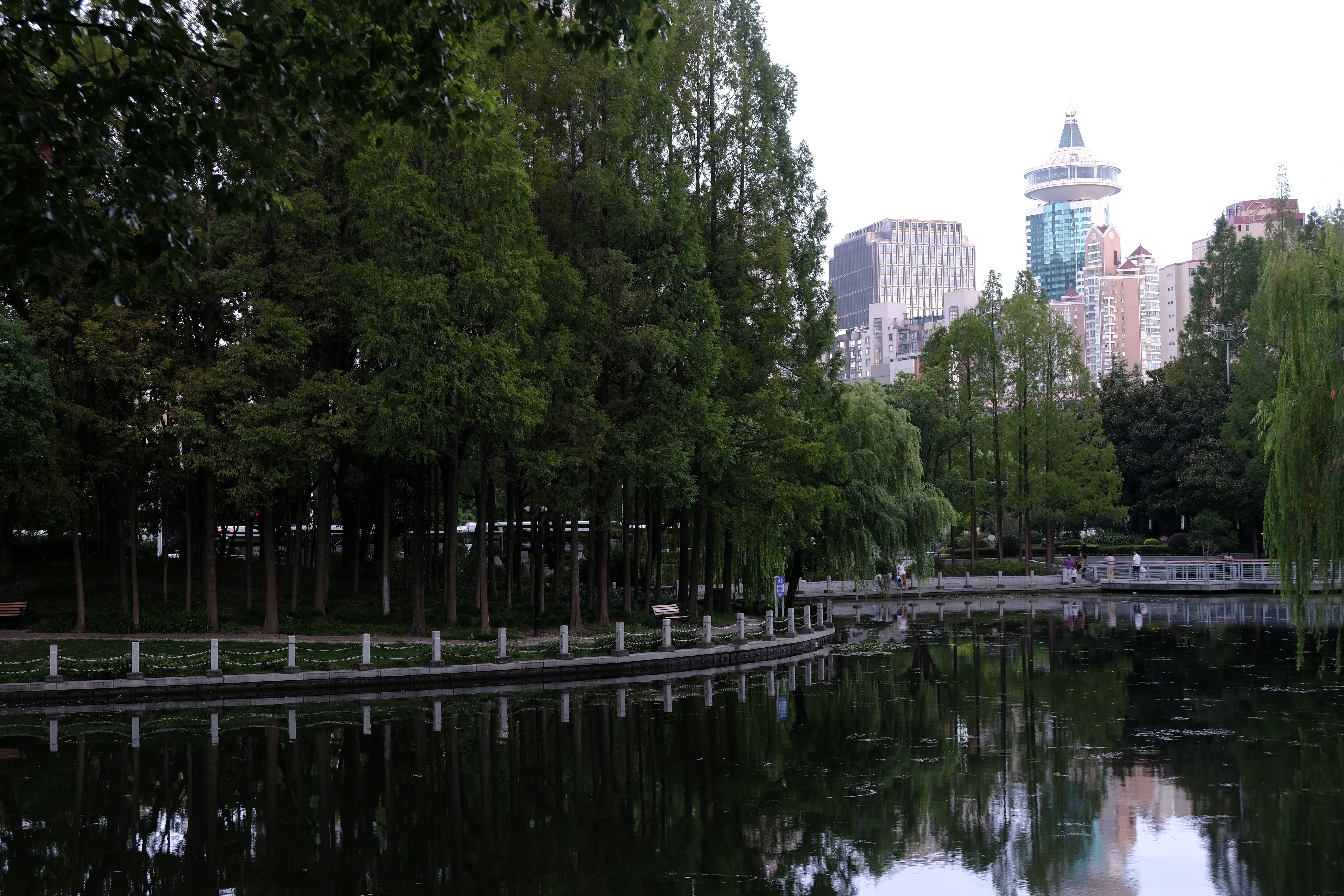 A tranquil park scene reflecting city skyscrapers and lush greenery in a calm pond. The juxtaposition highlights the harmony between urban life and nature.
