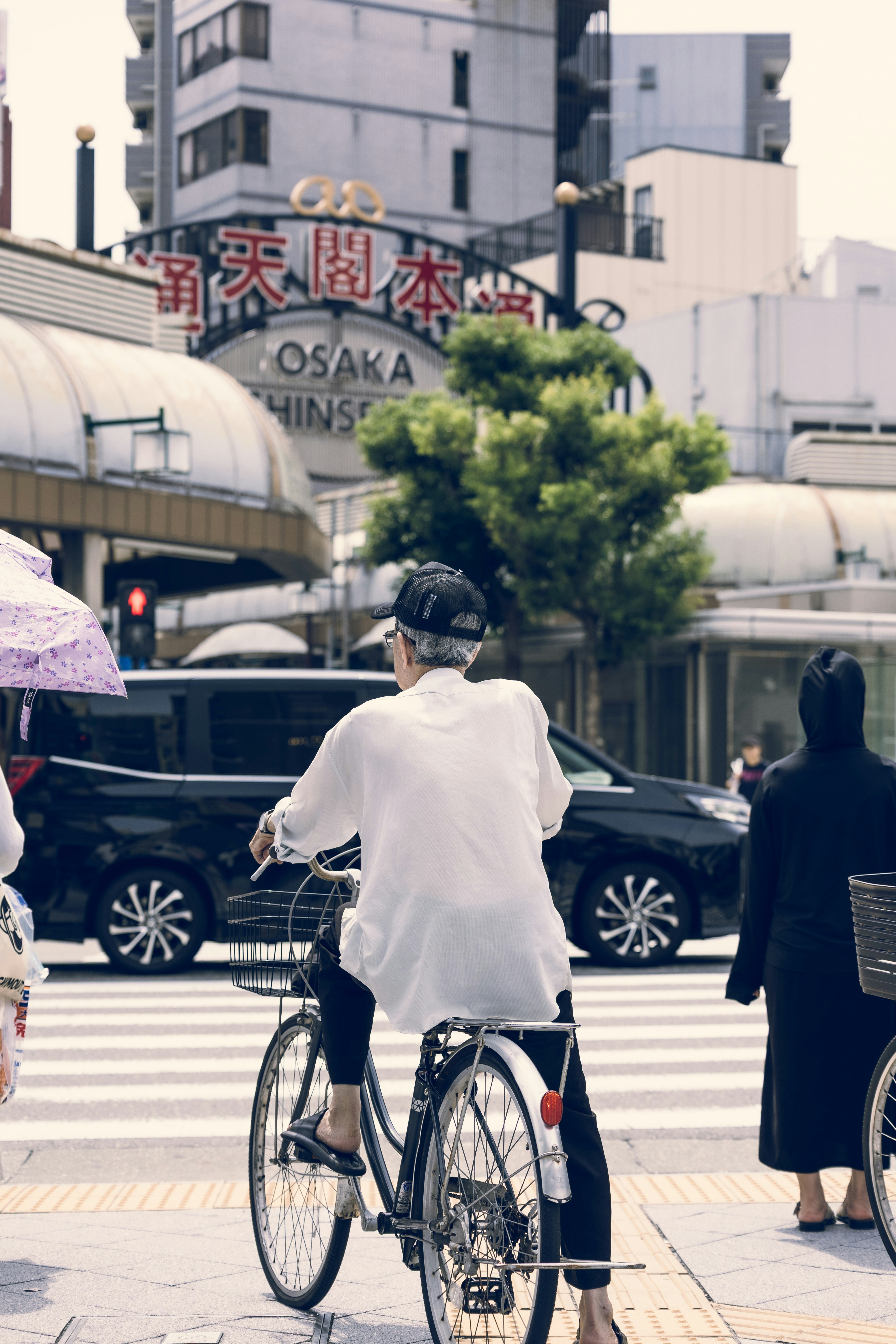 White-shirt Cyclist at Osaka Crosswalk: A Quiet Moment Amid City Traffic