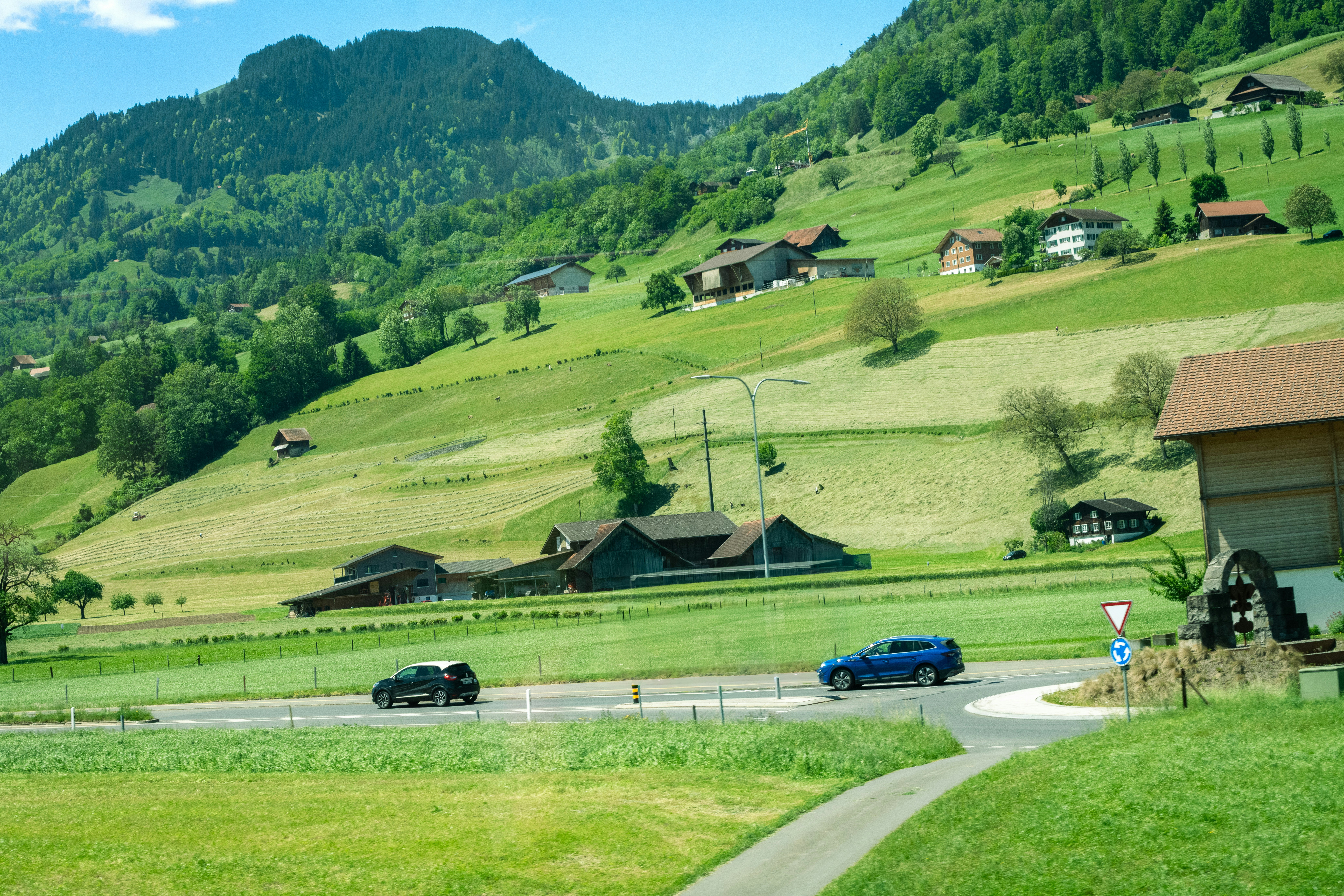 Cars driving on a road through green hills.