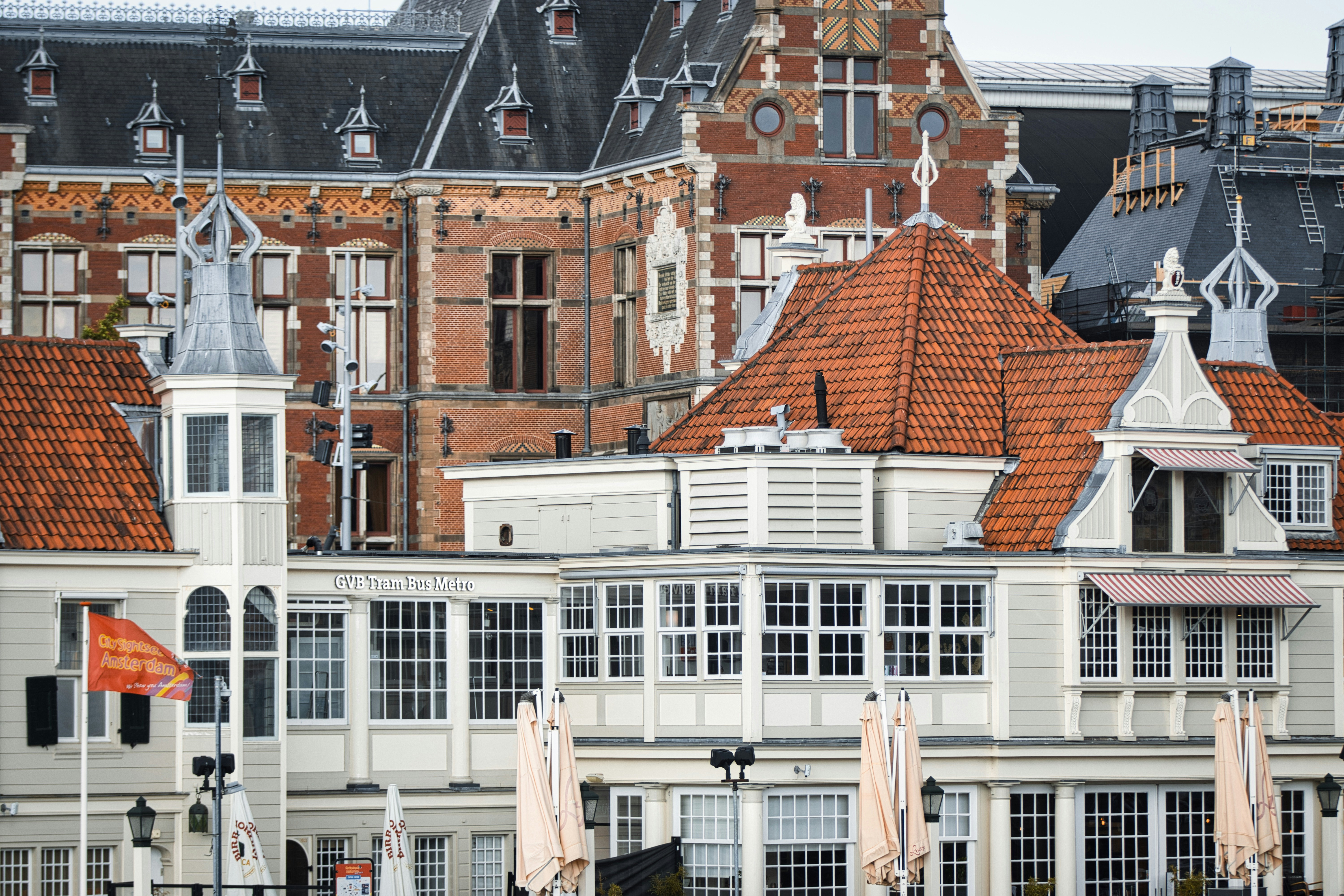 Historic buildings with distinct architectural styles featuring ornate rooftops and large windows. A flag flutters in the foreground.