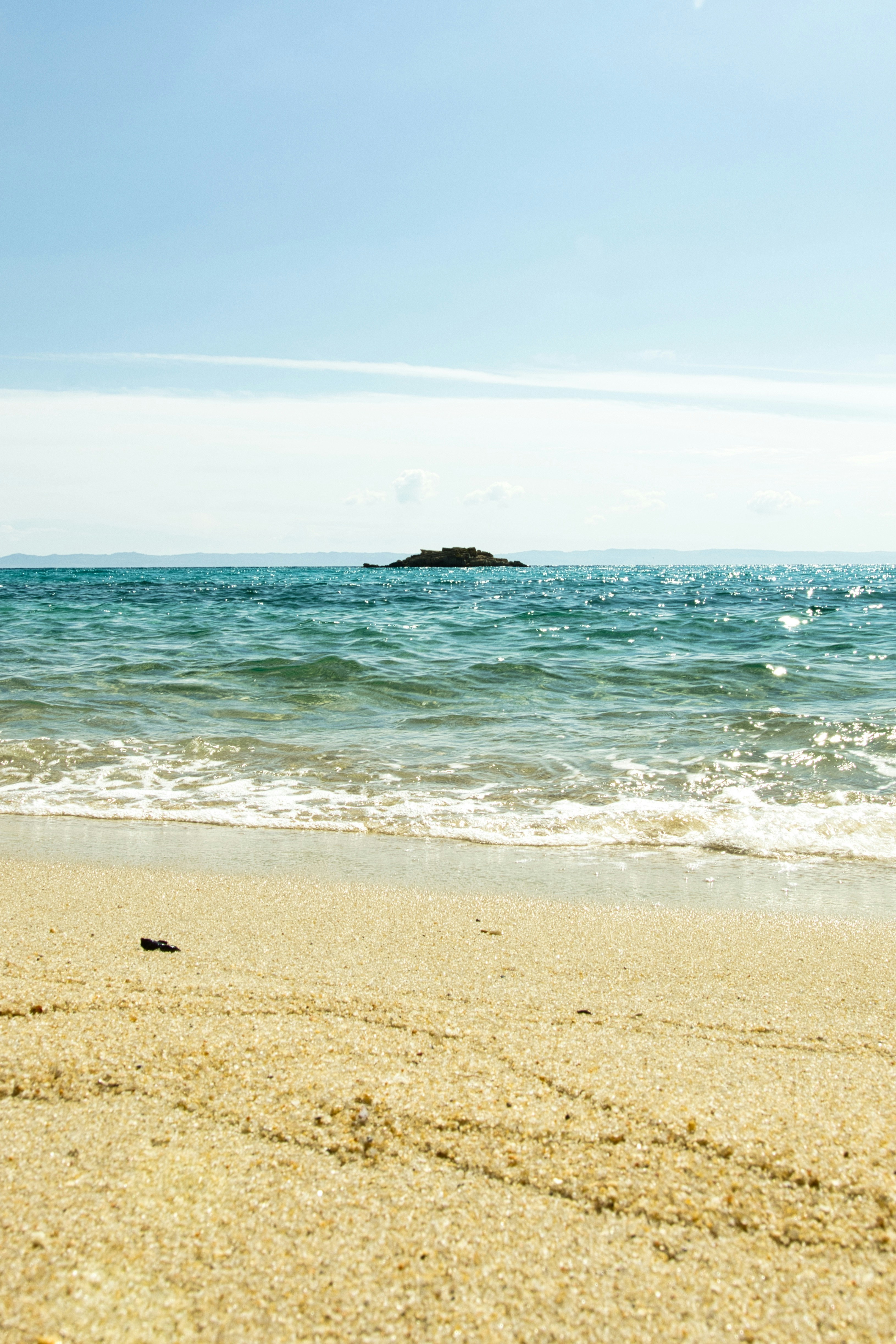 Sandy beach with ocean waves and distant island.