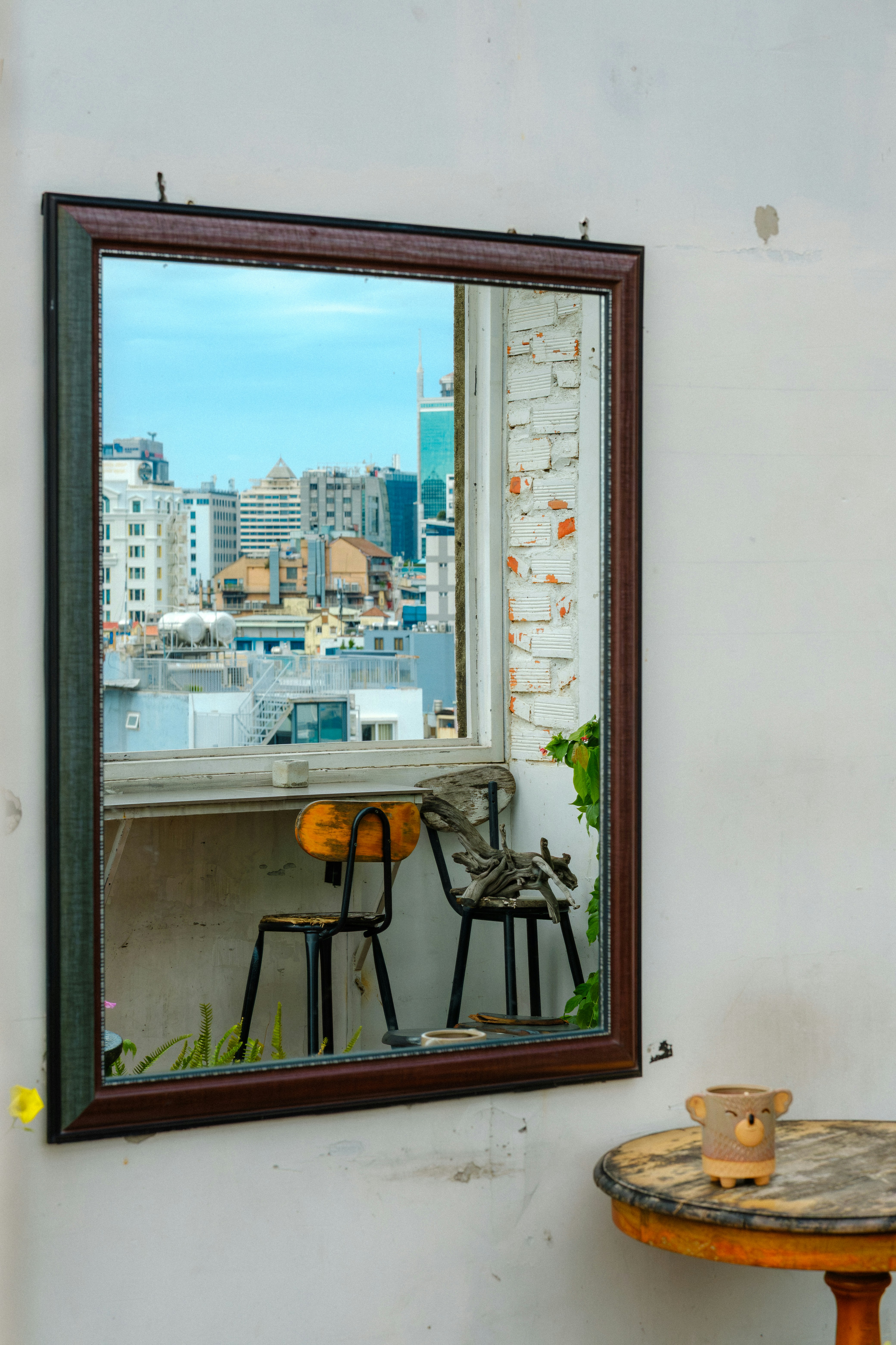Mirror reflects cityscape and two chairs on balcony.