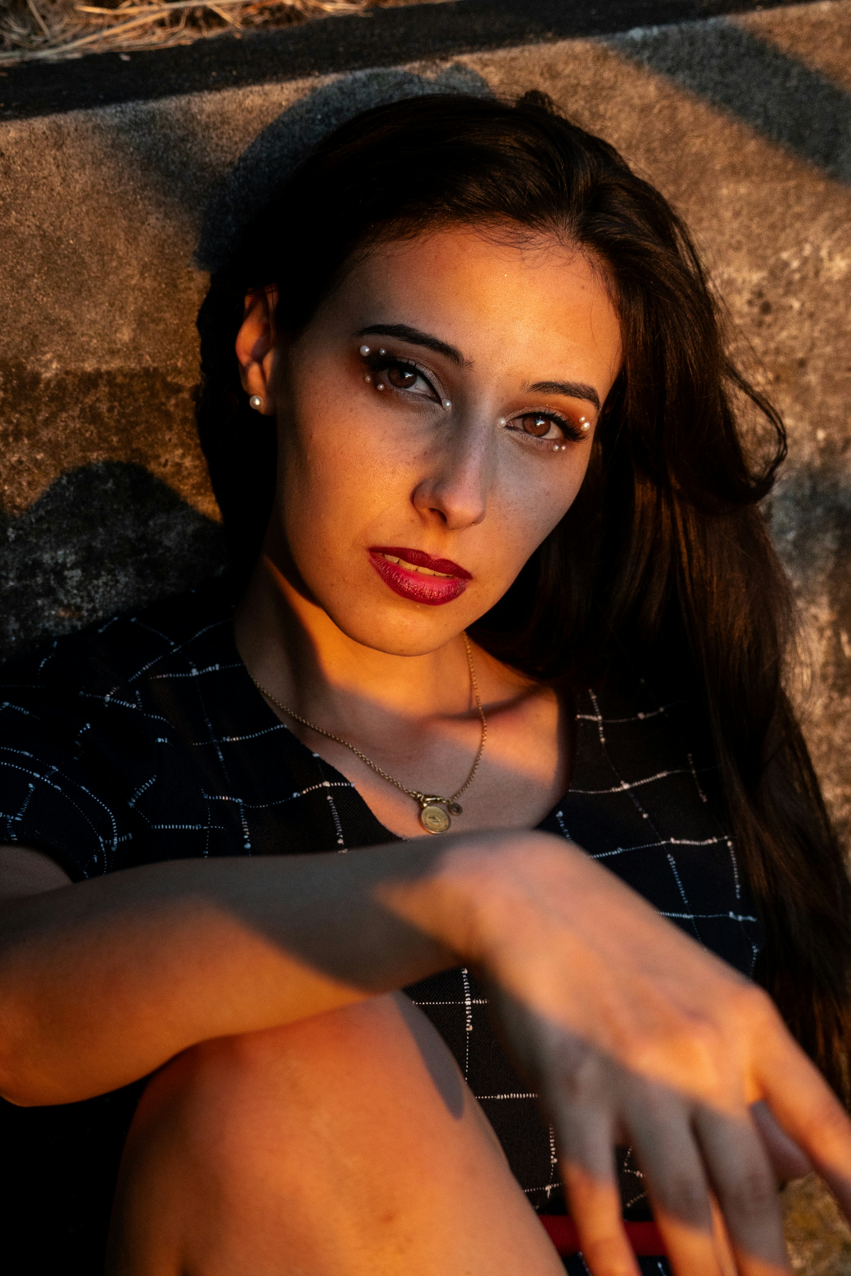 A woman gazes intently at the camera, illuminated by warm sunset light, with her hair cascading over her shoulder. The scene captures a moment of serene beauty and introspection.