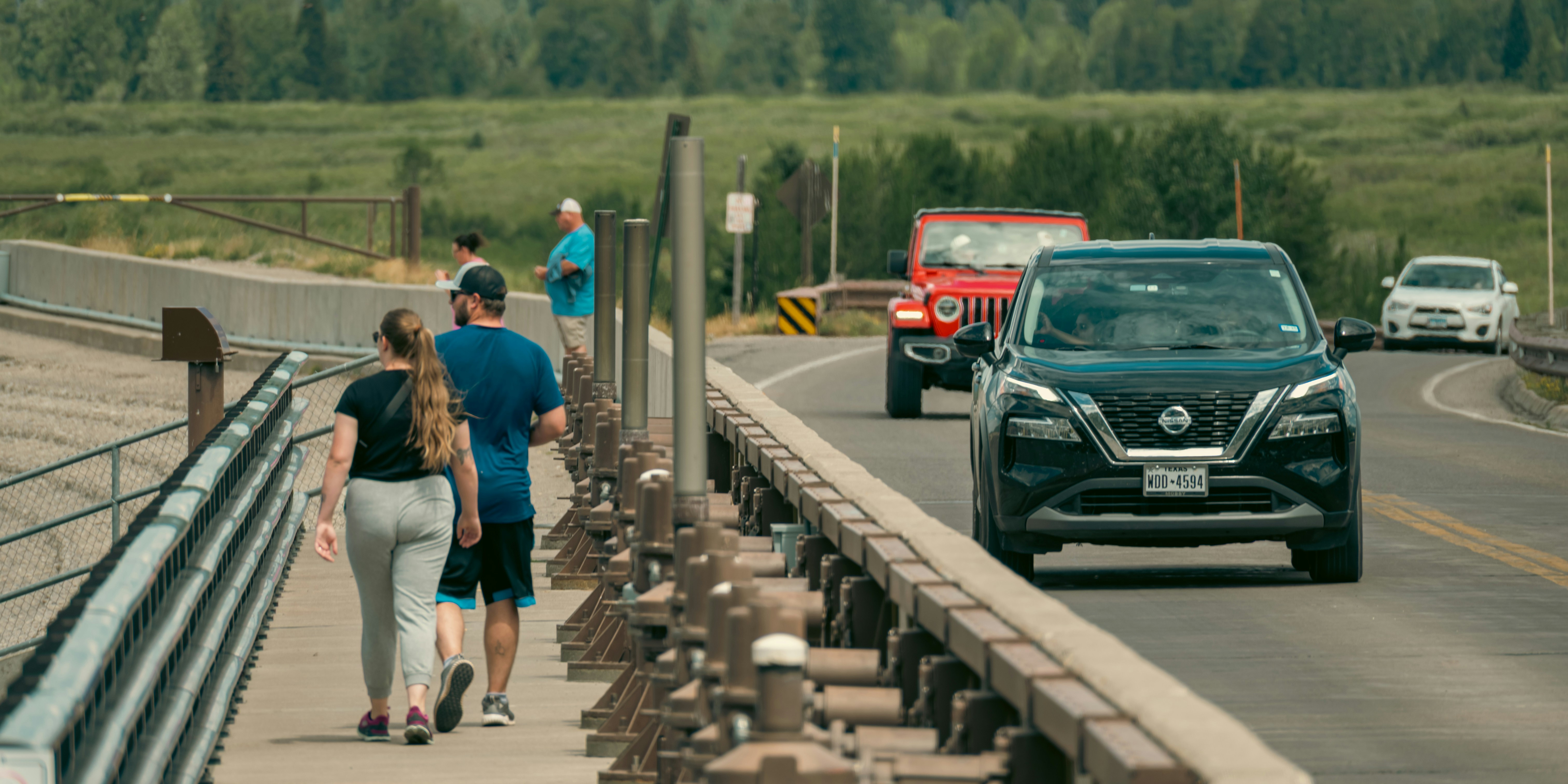 People walk on a bridge with cars driving by.