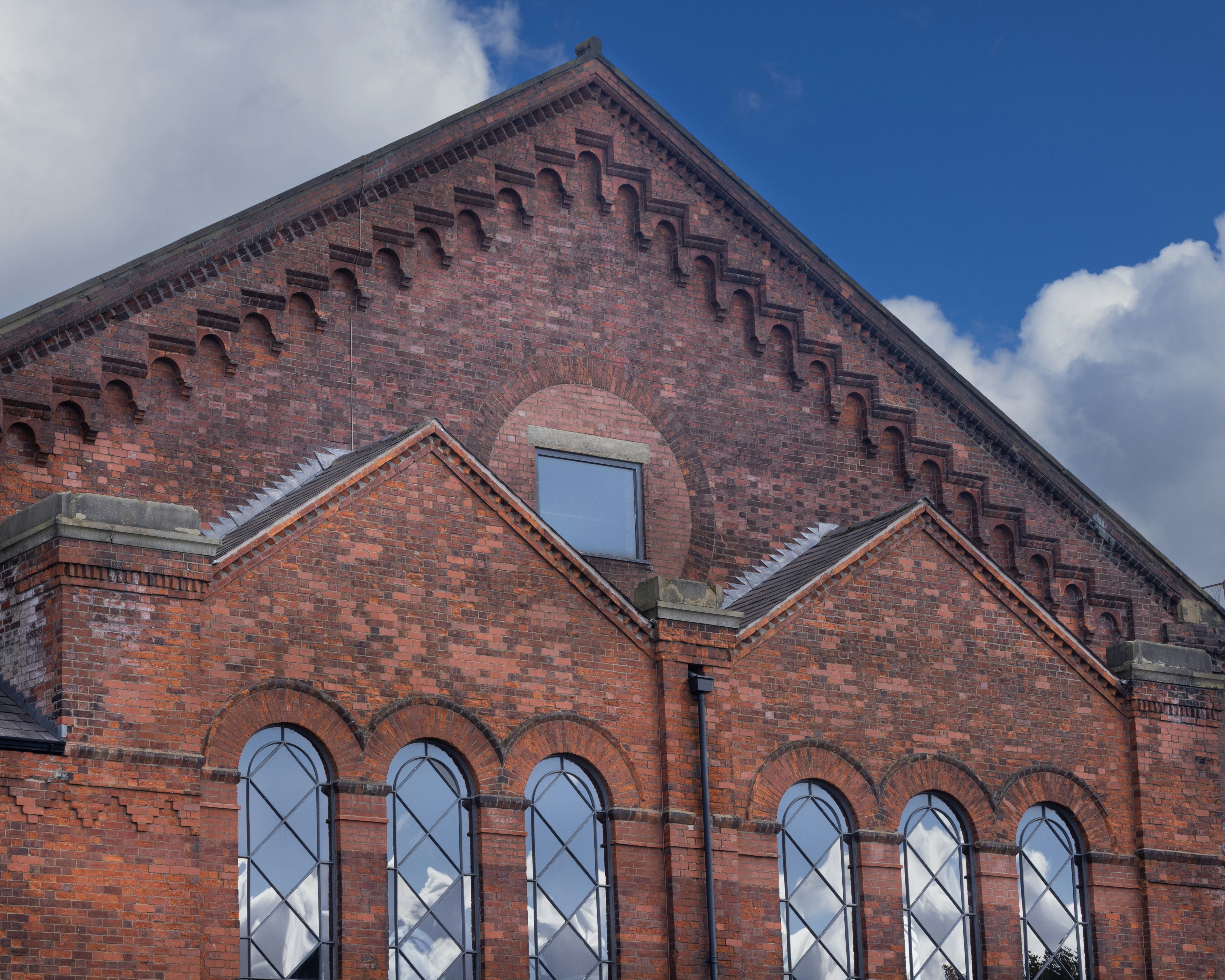 Charming neighbourhood of Manchester | Red brick building with arched windows under blue sky.