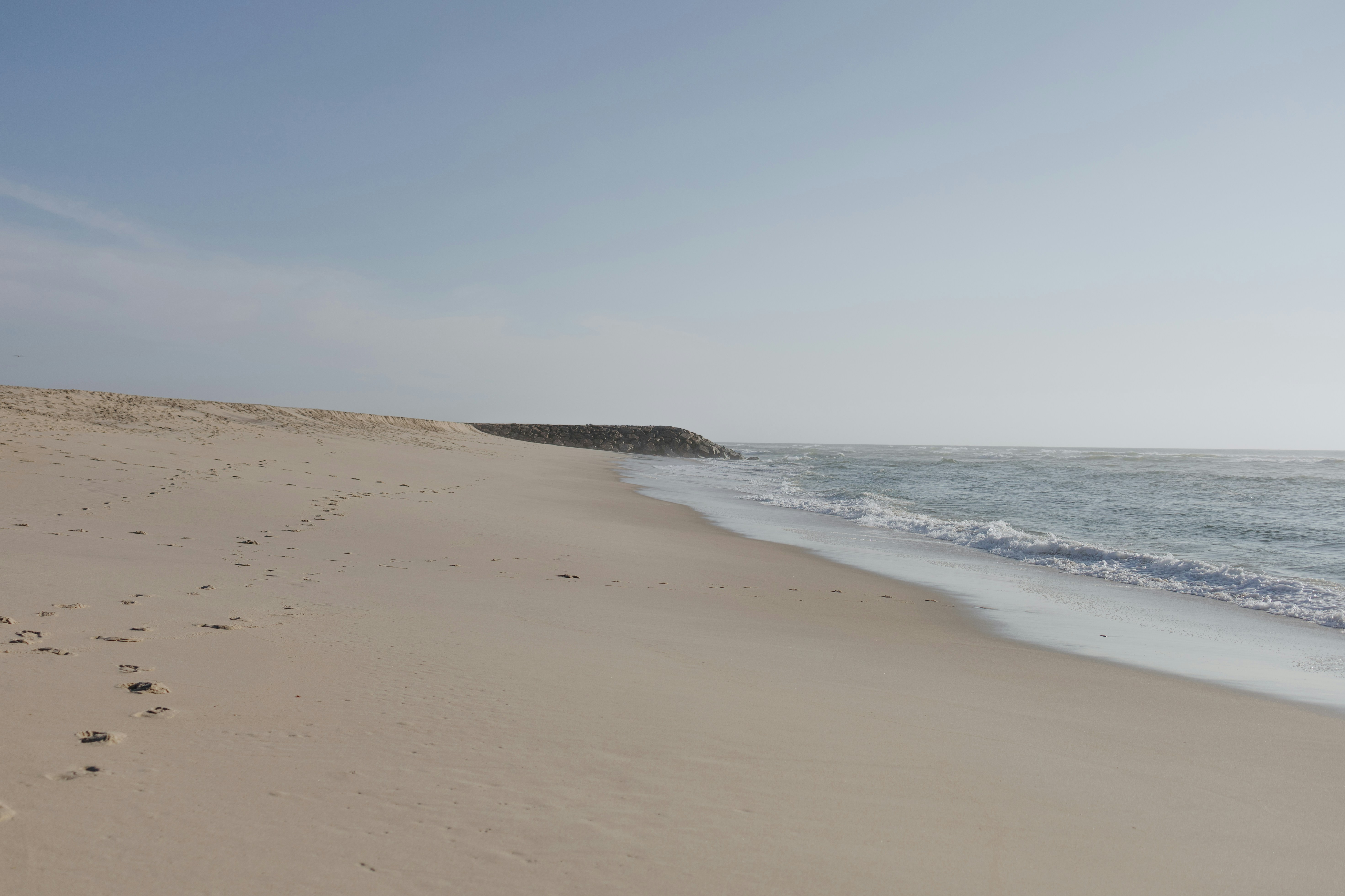 Sandy beach with gentle waves and a breakwater.