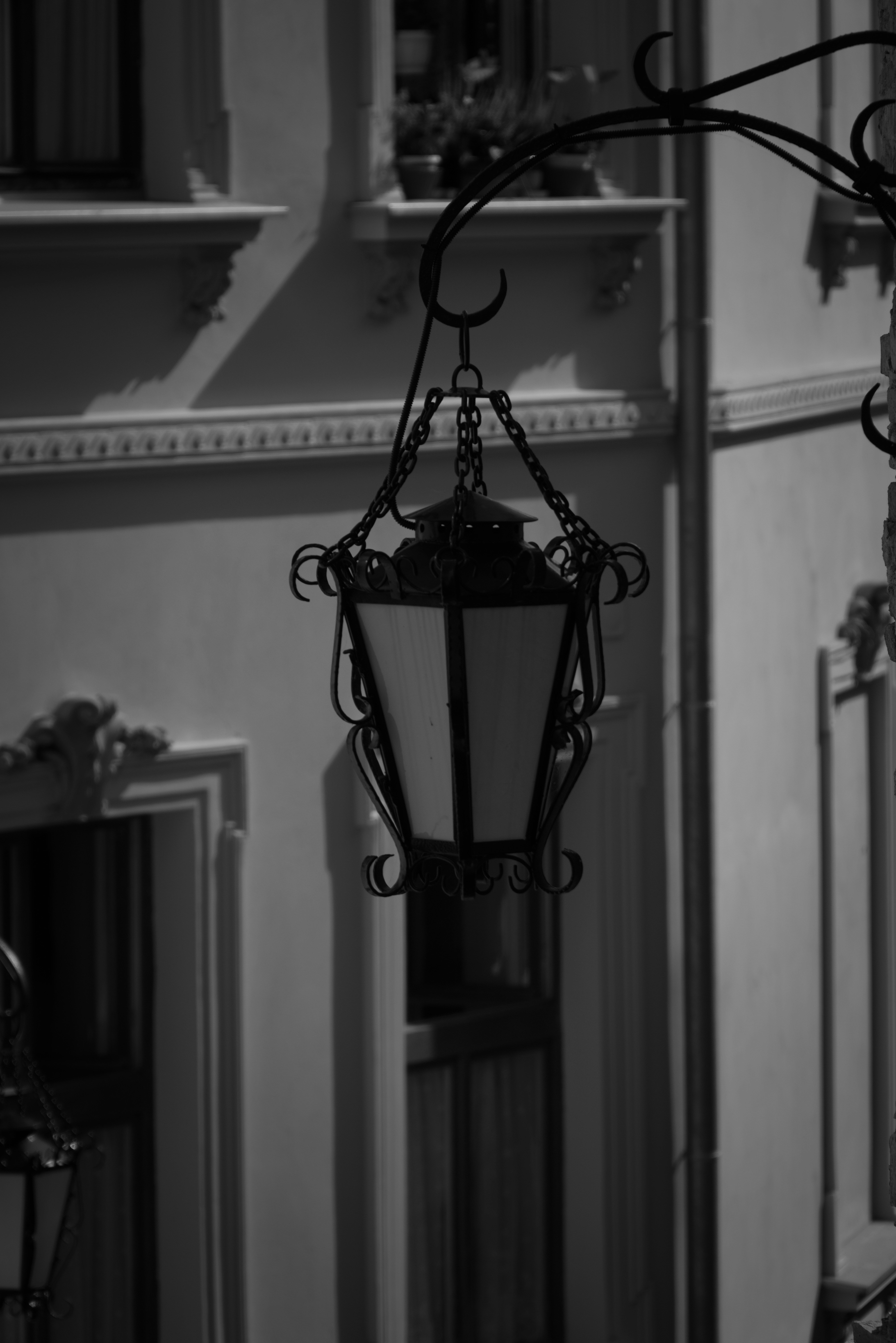 Intricate black lantern hanging against a backdrop of architectural details, showcasing vintage charm and craftsmanship.