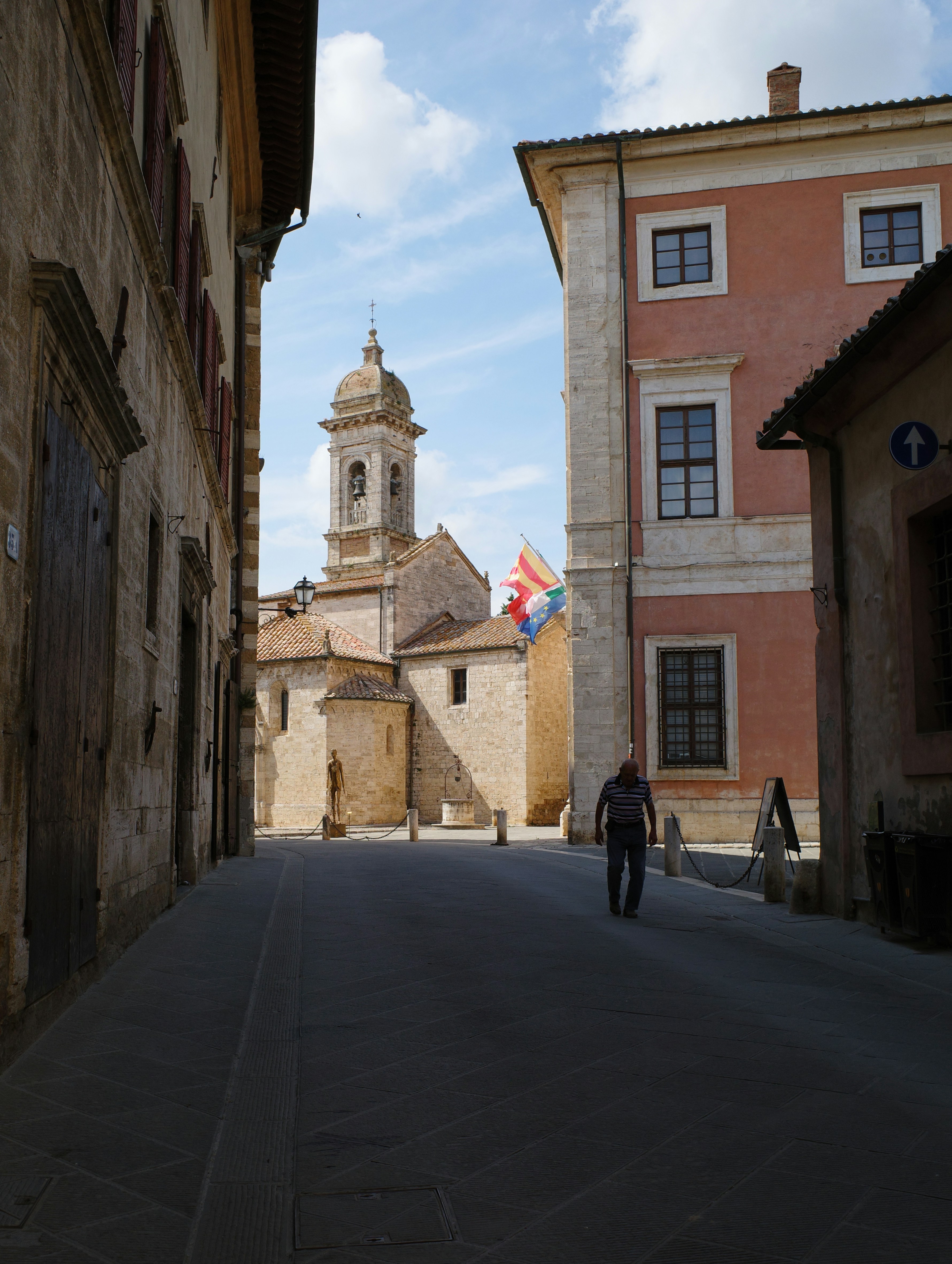 Man walks down a sunny street towards a church.
