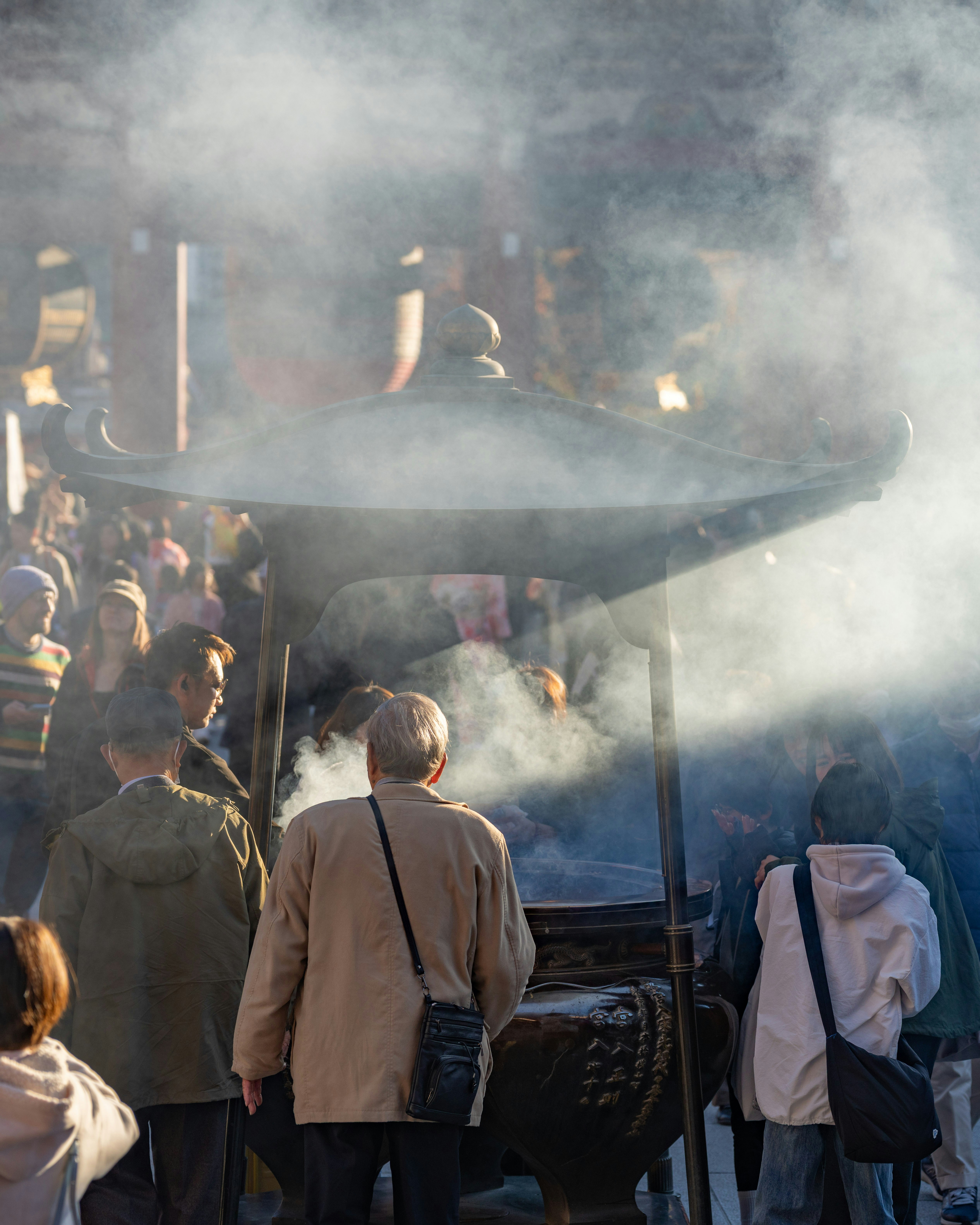 People gather around a smoking incense burner at a temple.