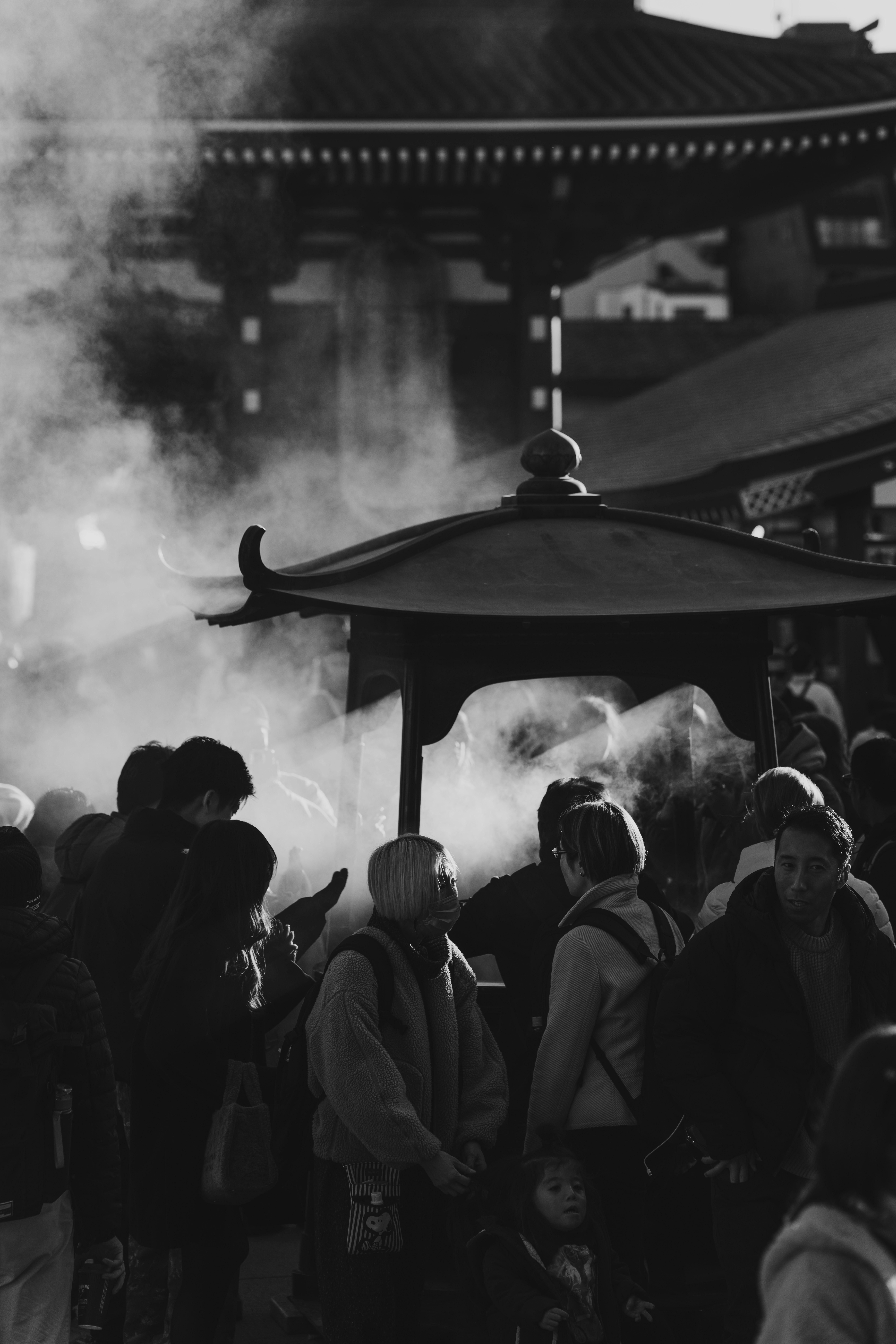 People gathered around a smoking incense burner at a temple.