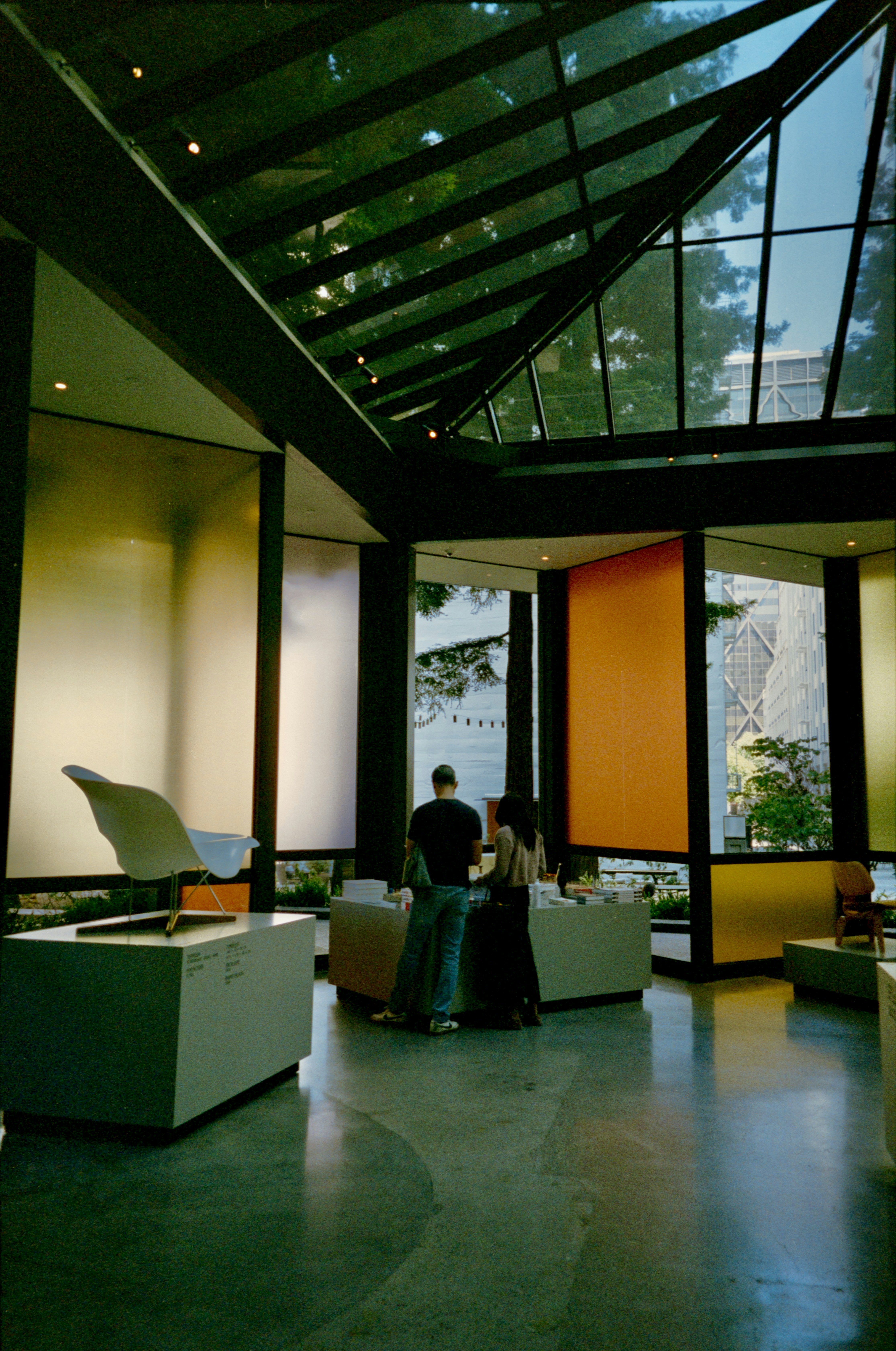 Two visitors engage in conversation amidst a modern gallery showcasing vibrant colored panels and elegant furniture. The interplay of light and shadow enhances the contemporary atmosphere.