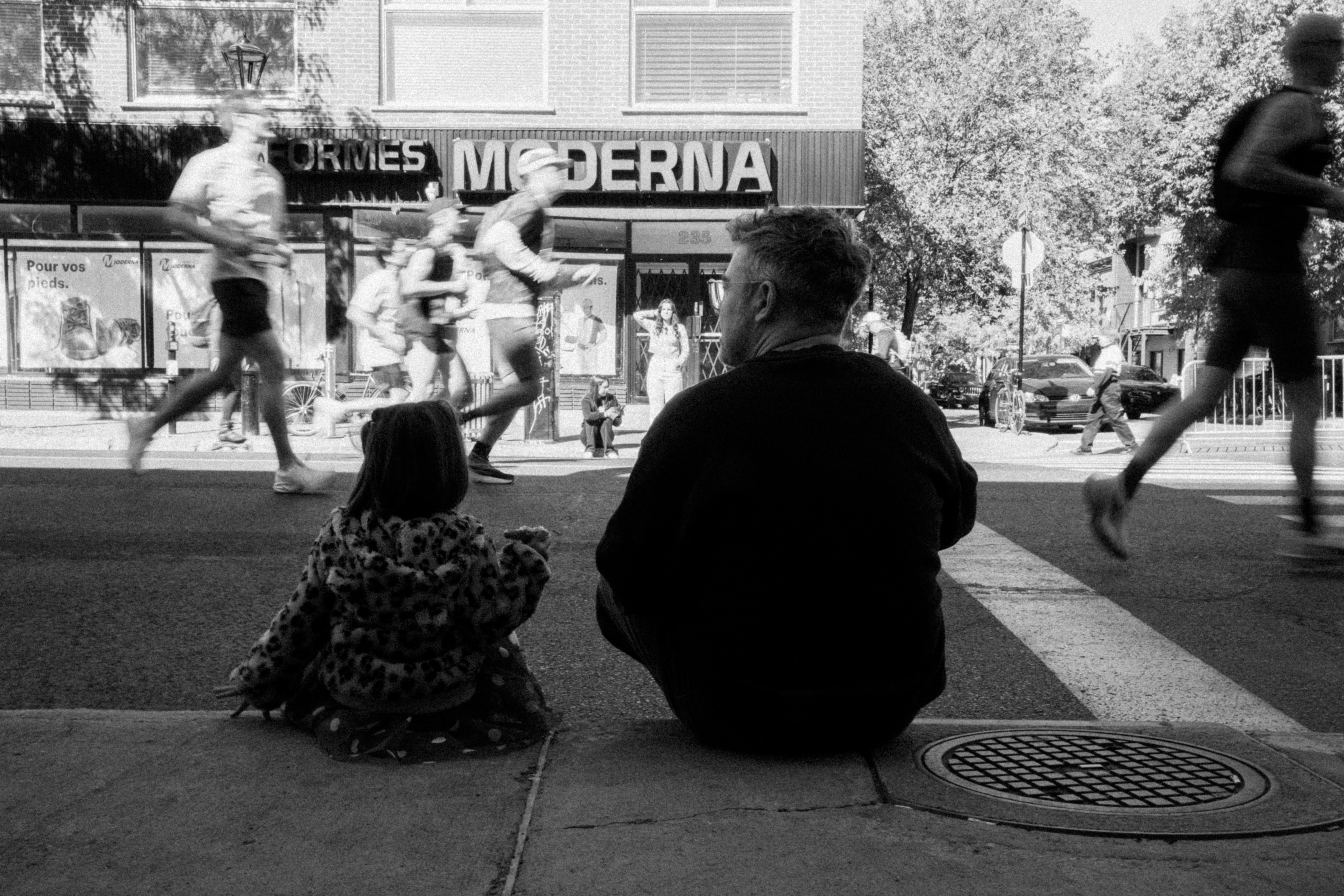 Man and child watch runners pass by building.