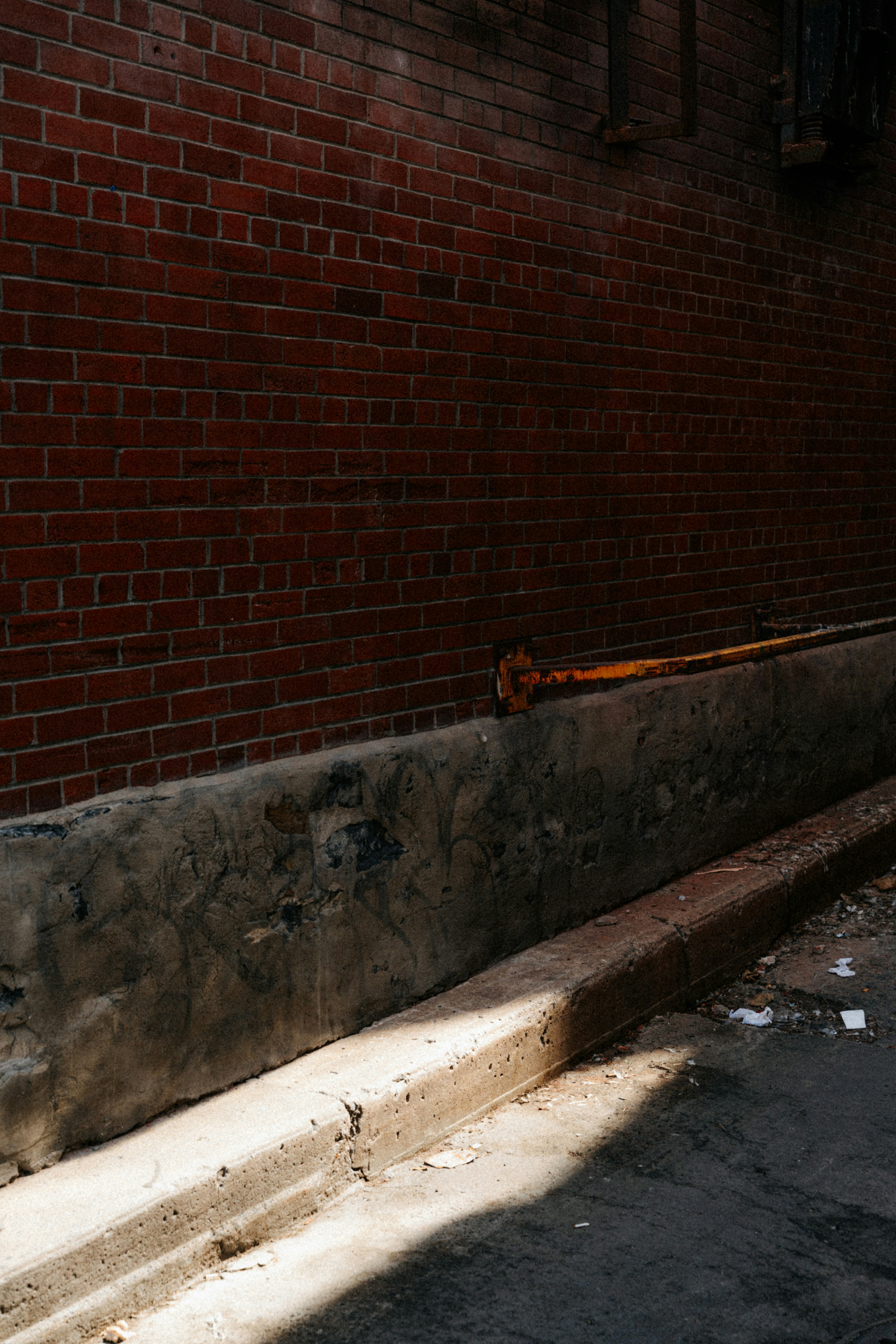 Sunlight streams onto a brick wall and concrete gutter.