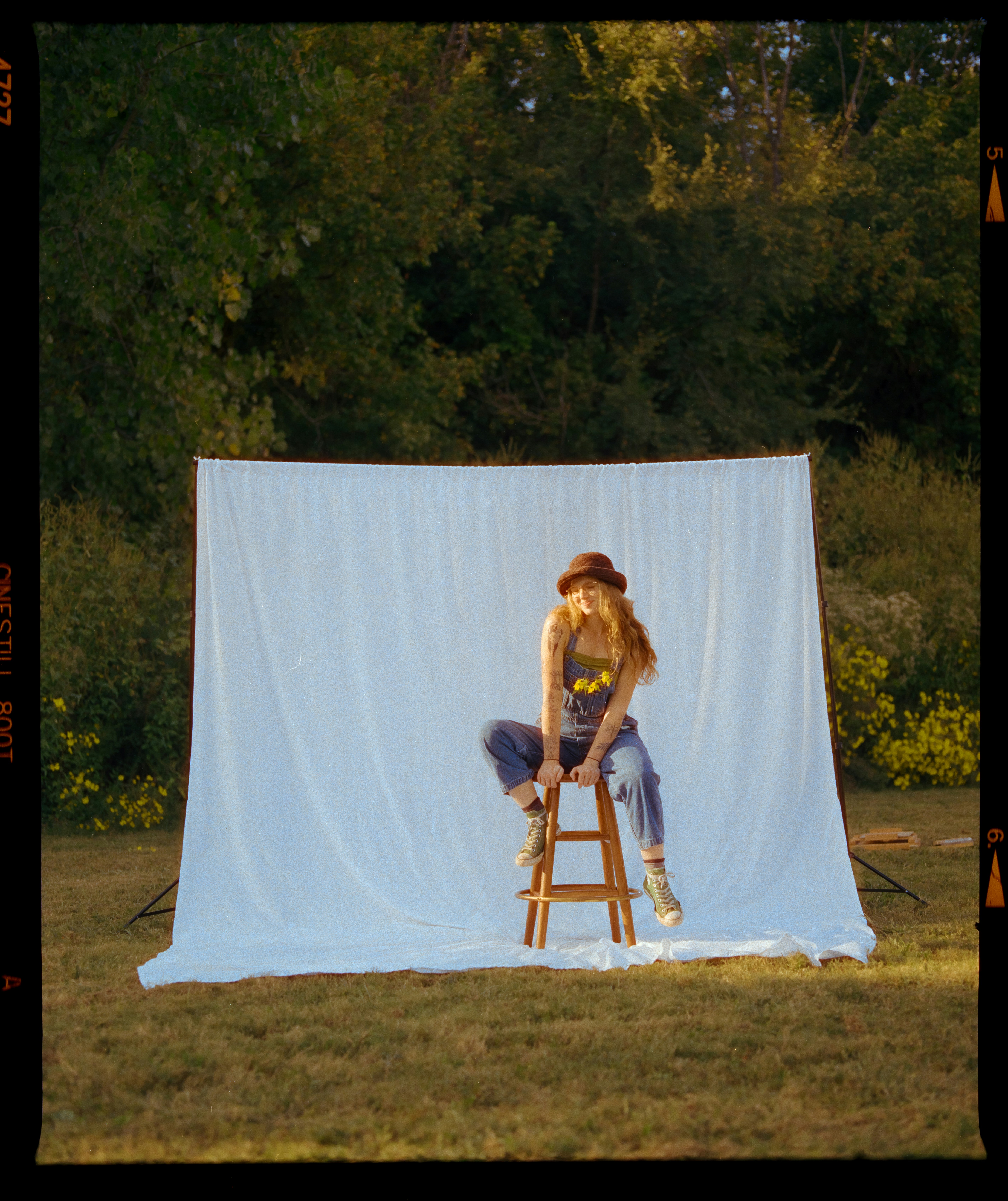 Field-side Studio Portrait: Woman in a Hat on a Wooden Stool Before a White Backdrop