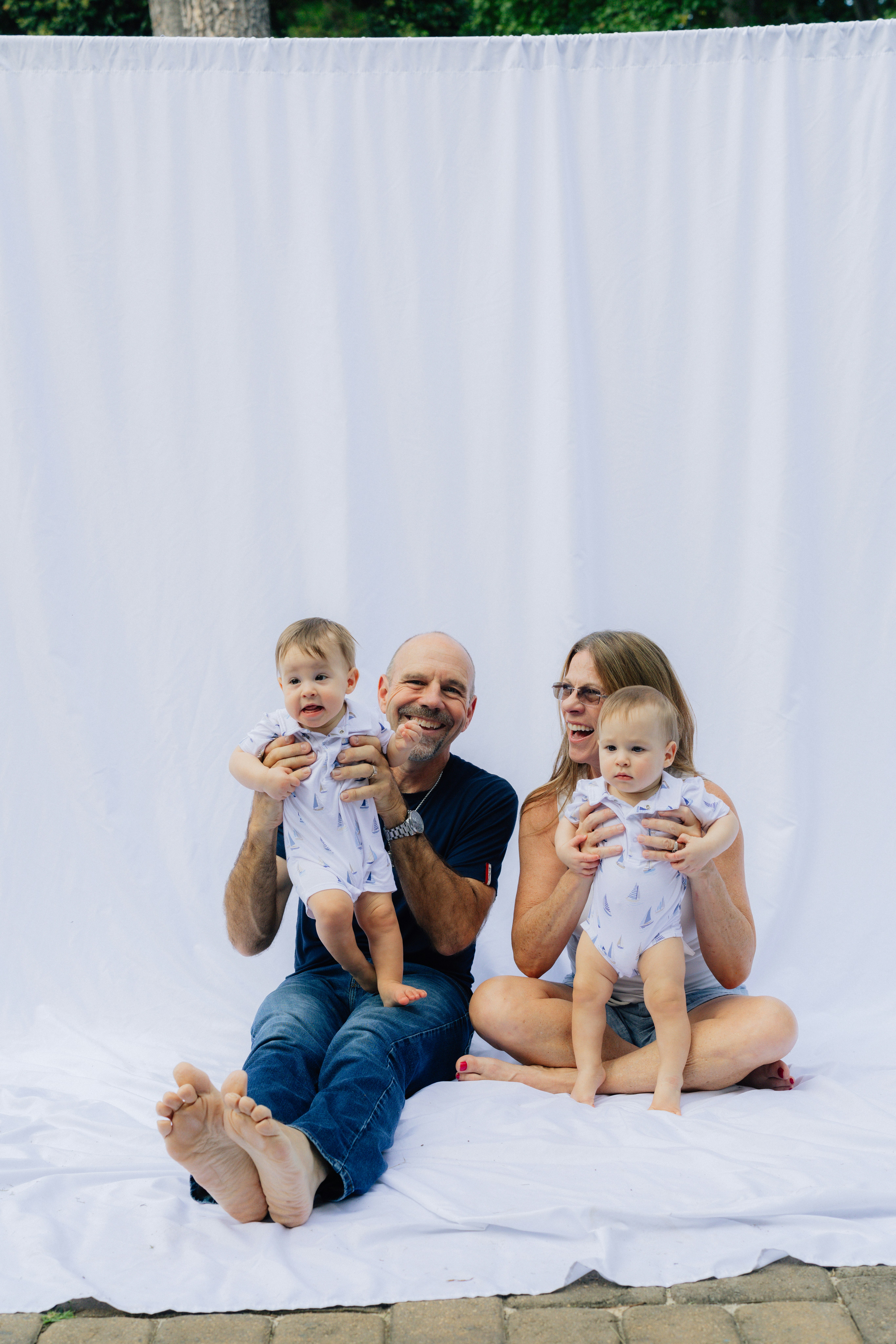 Daylight Family Portrait: Parents Cradle Two Babies Against a Pristine White Backdrop