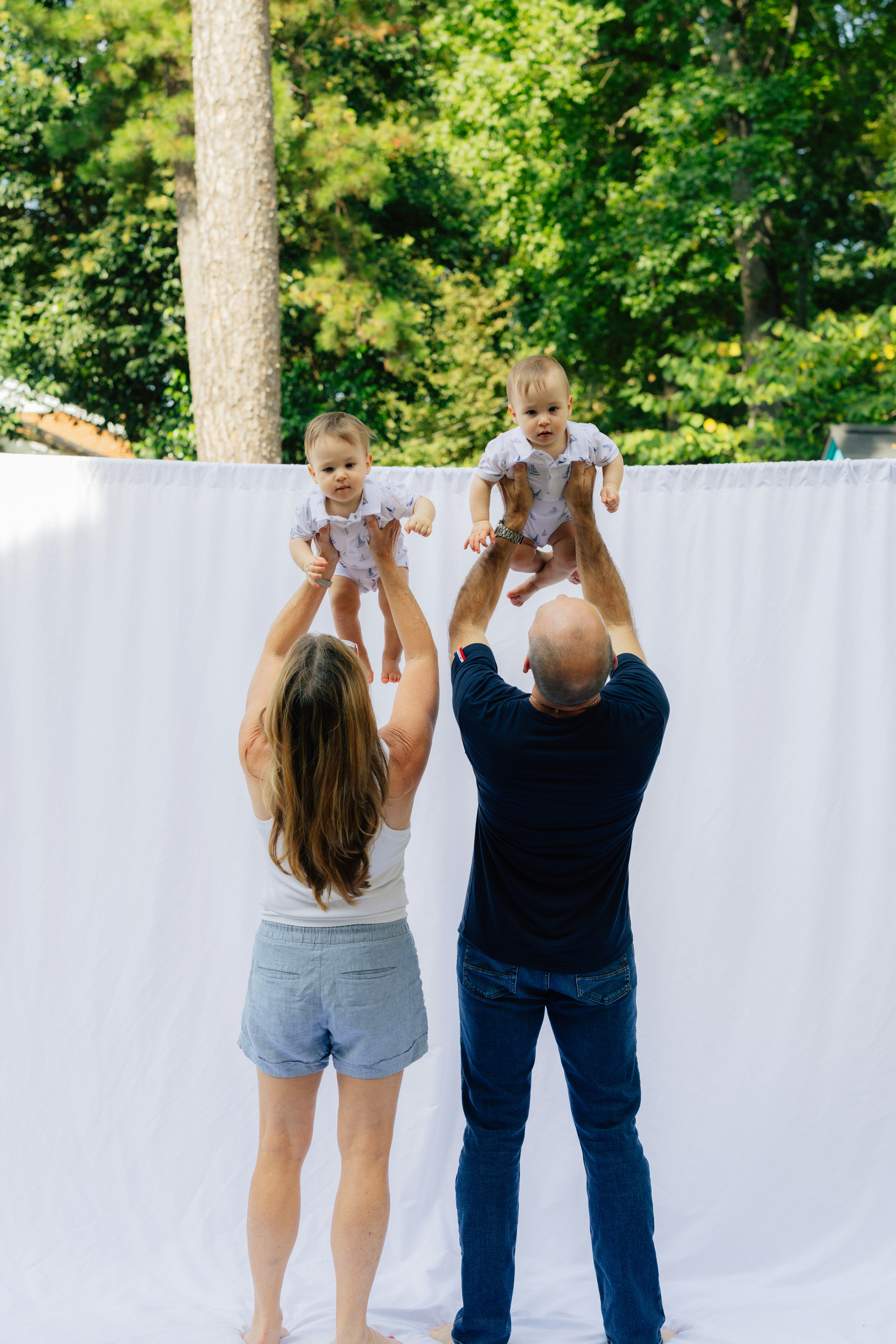 Upward Joy: Two Babies Raised by Their Parents Over a White Backdrop