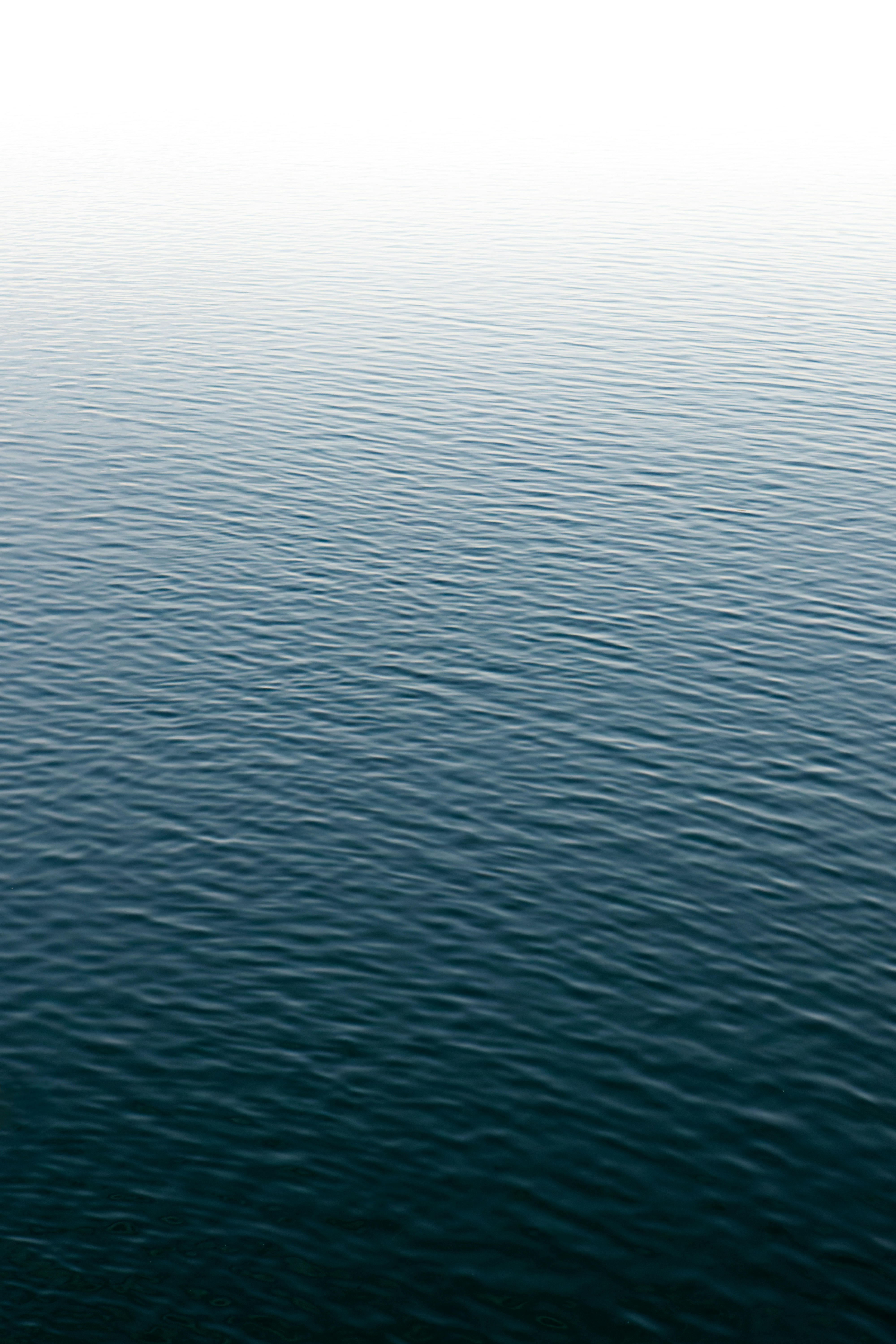 Calm water surface reflecting soft light, creating a gradient from deep blue to white. Ideal for evoking a sense of peace.