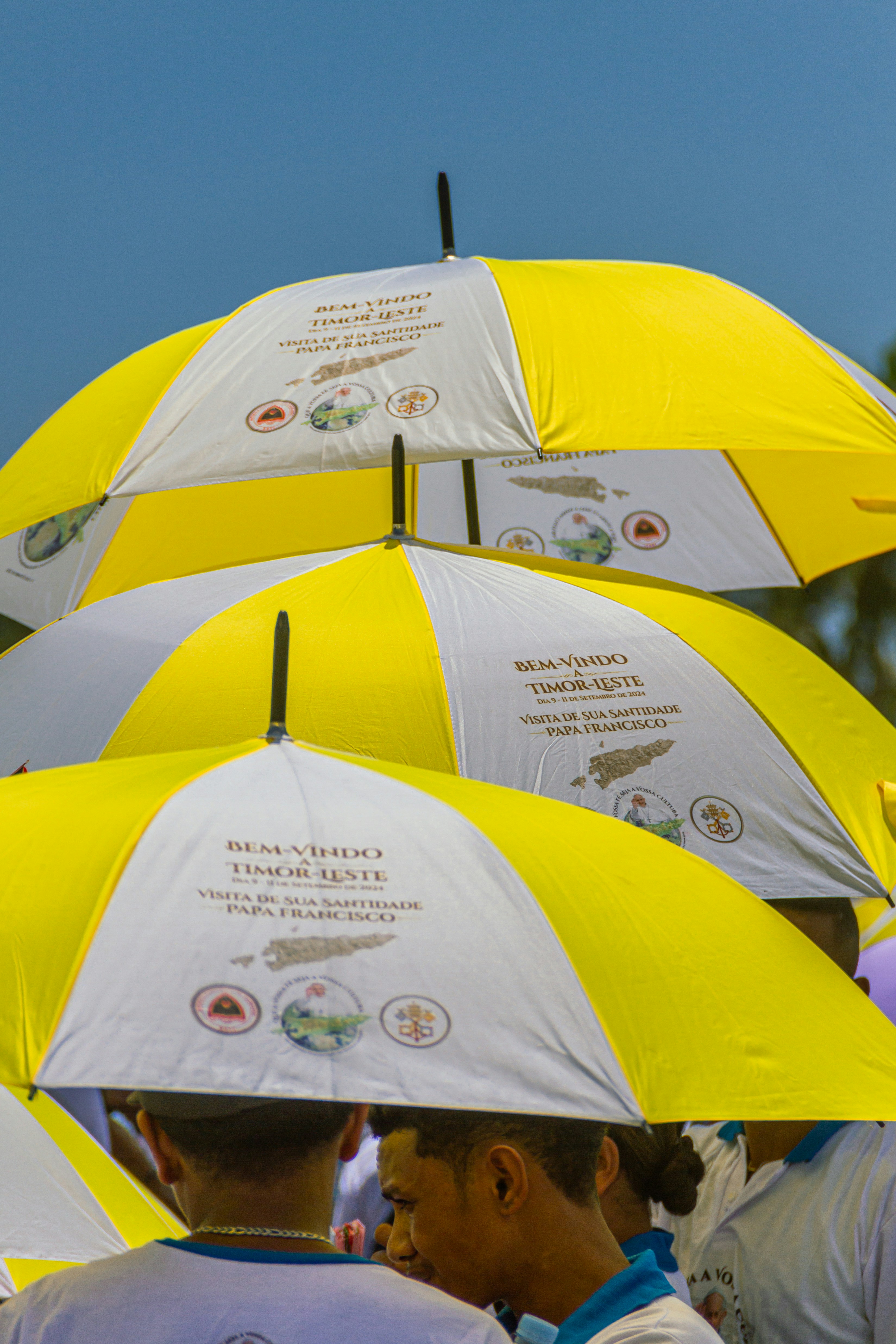 Colorful umbrellas featuring a welcoming message for visitors, creating a vibrant atmosphere at an event. The scene captures the spirit of community and celebration.