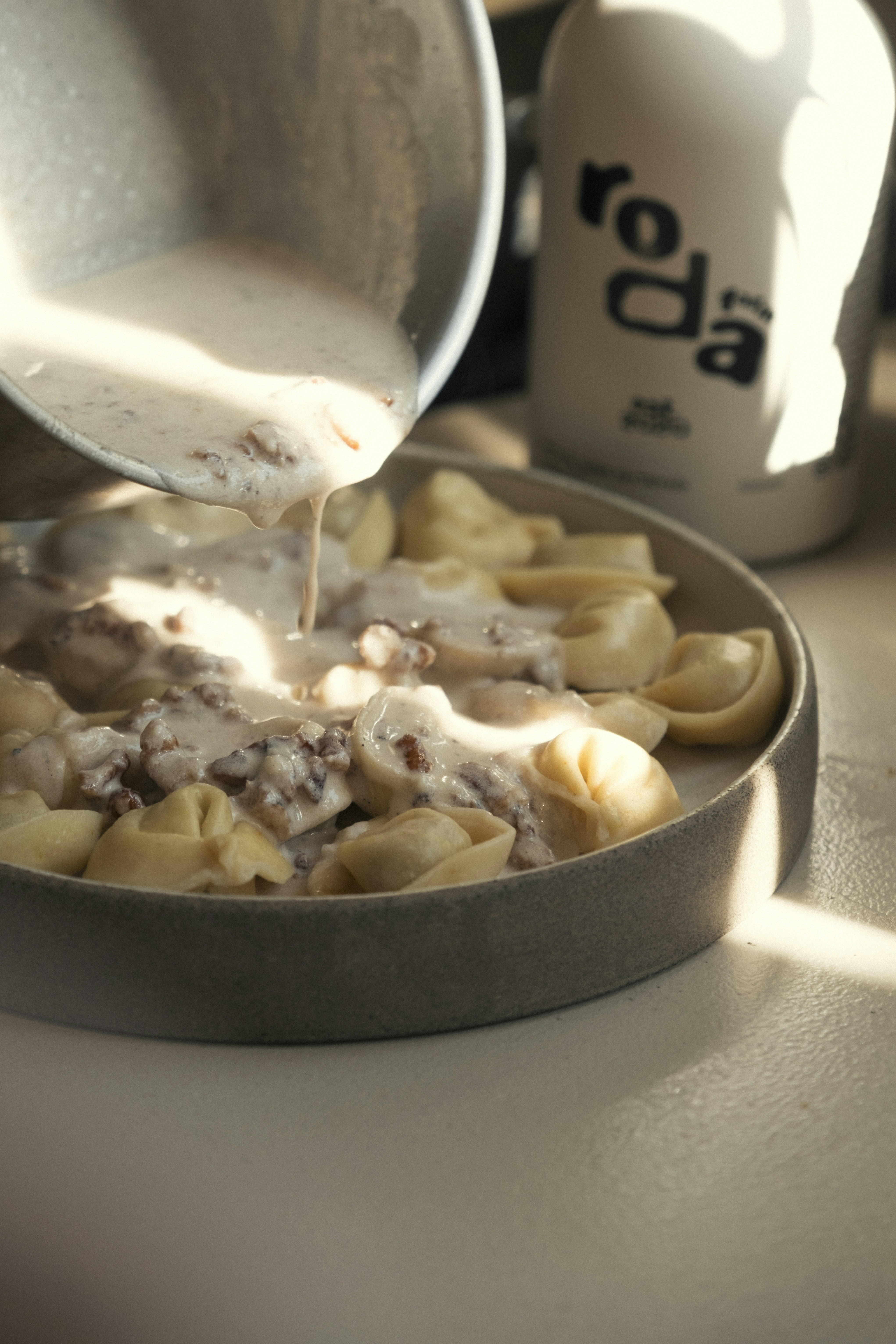 Pure olive oil from the Mediterranean, crafted for organic food lovers and healthy cuisine. | Pouring creamy sauce over tortellini pasta in a bowl.