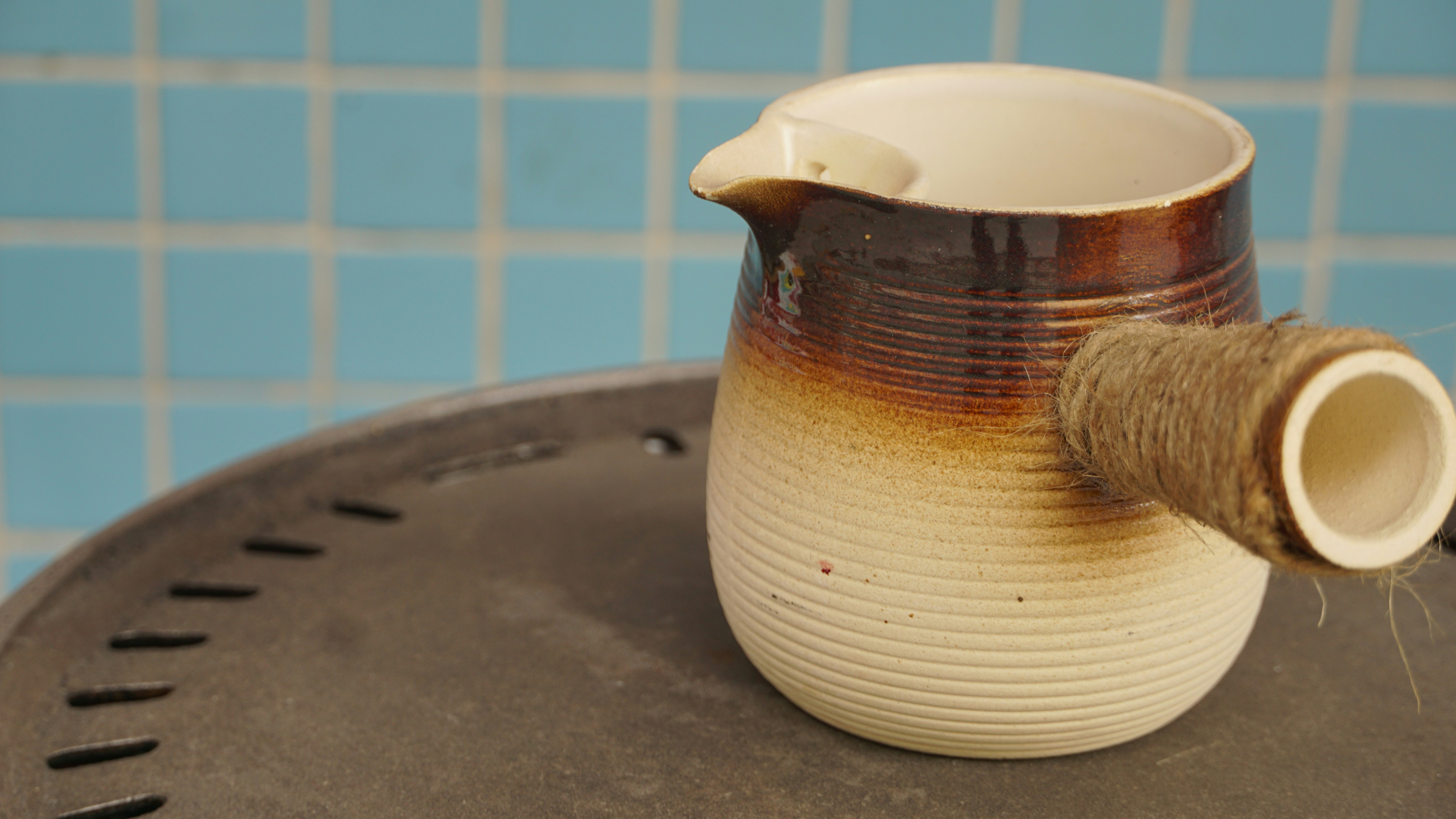 A ceramic pitcher with brown glaze and twine handle.