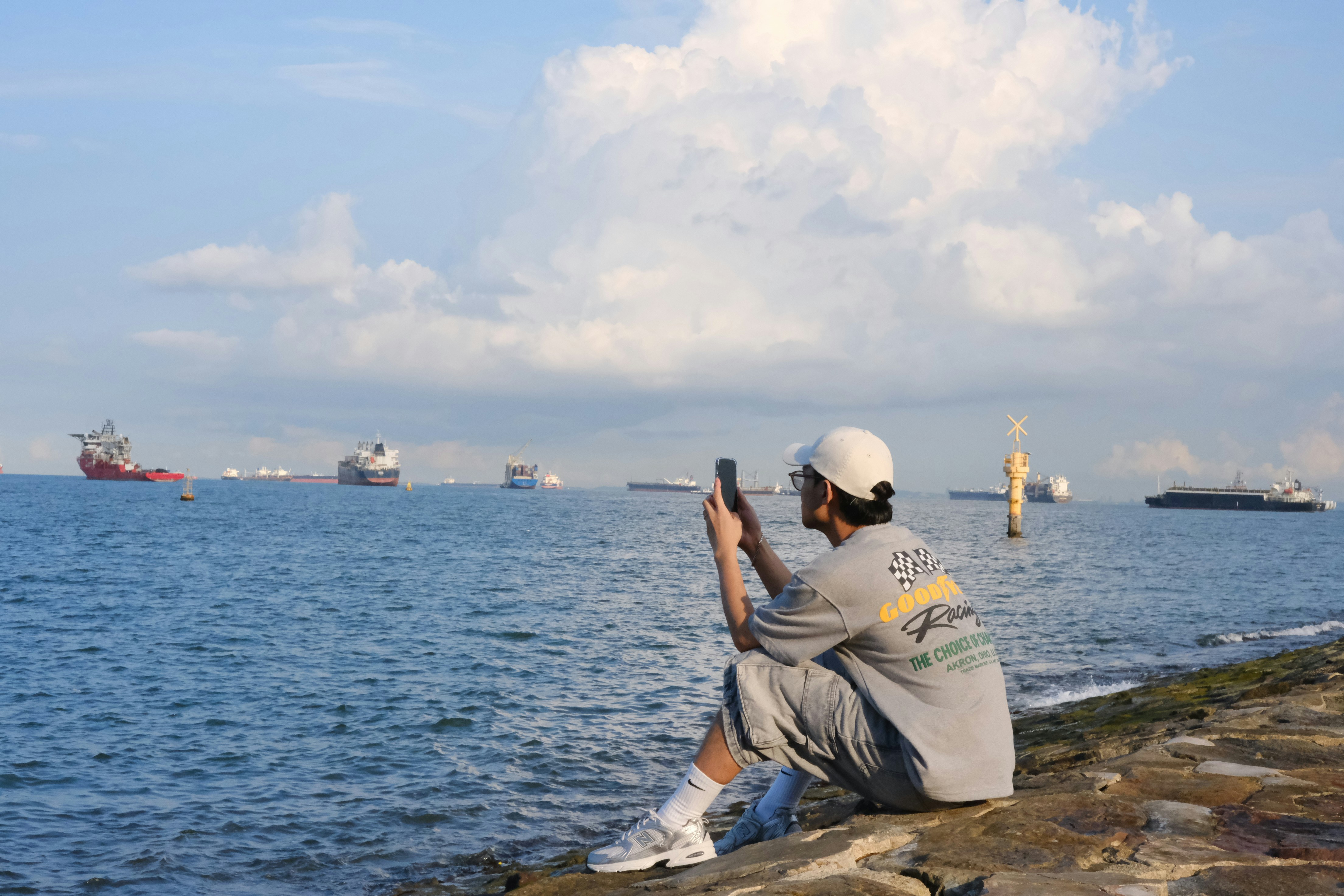 Man with phone watches ships on the sea.