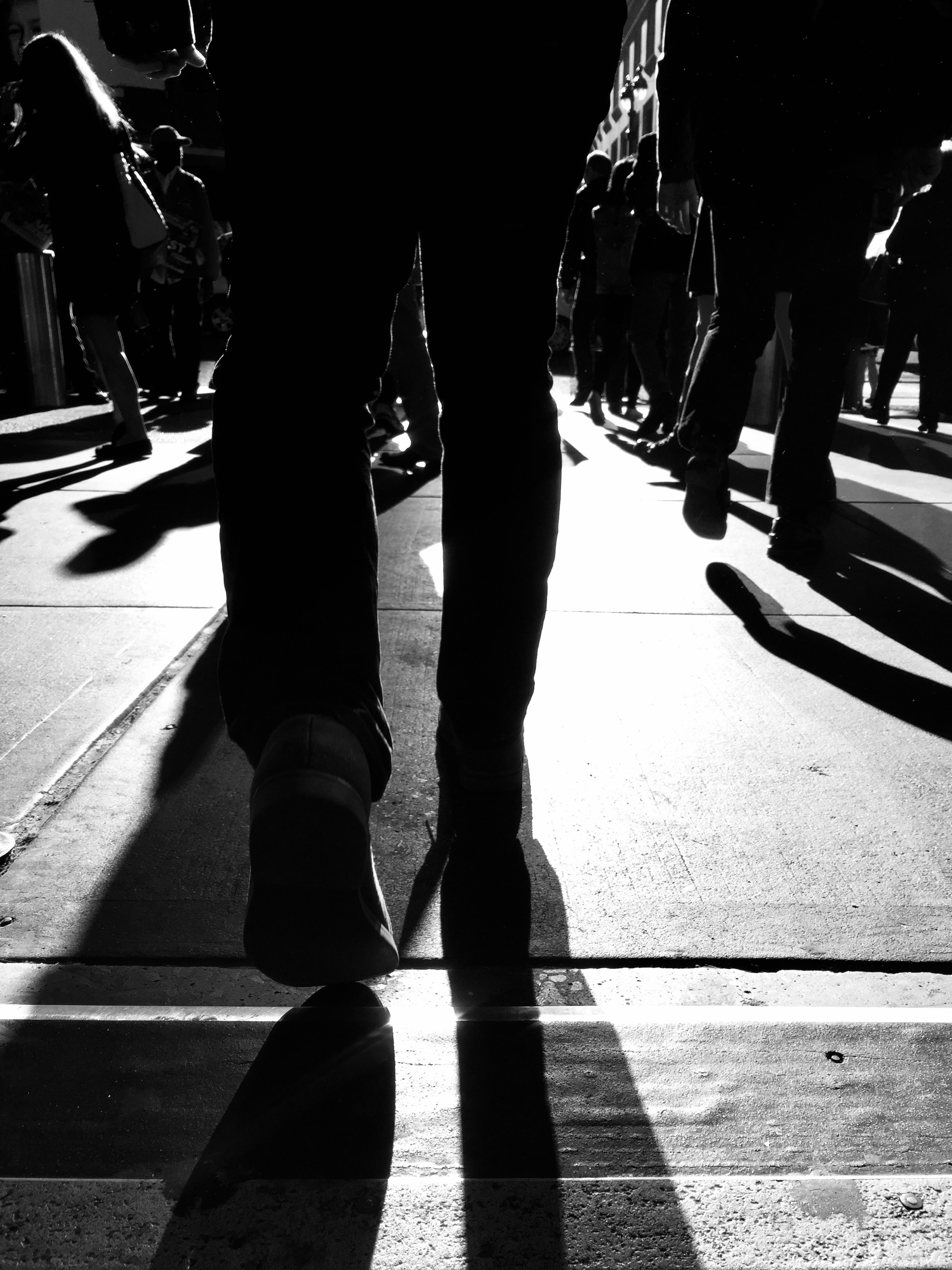 Silhouetted legs walking on a sunlit sidewalk