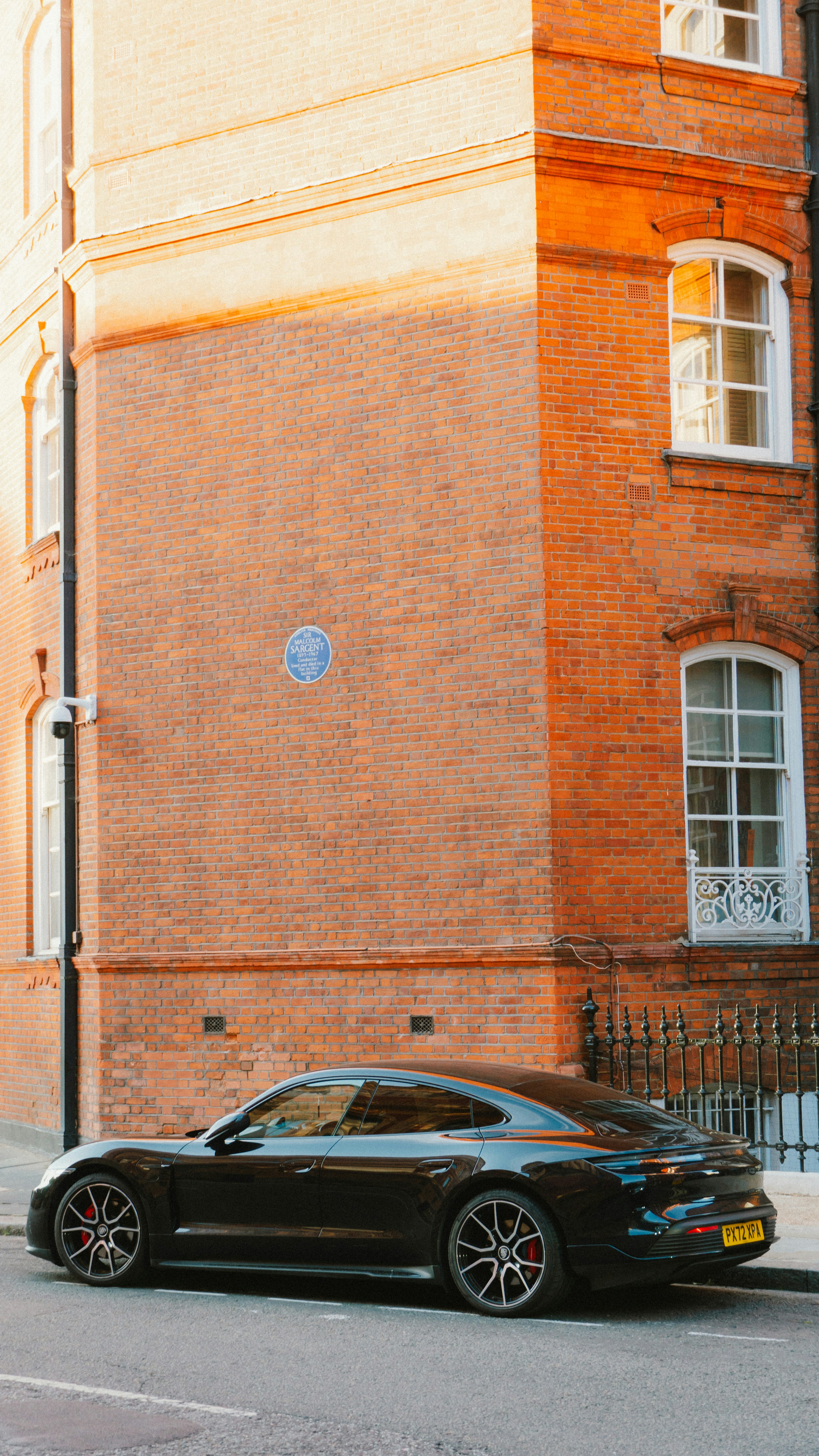 Black porsche parked on a street next to brick building.