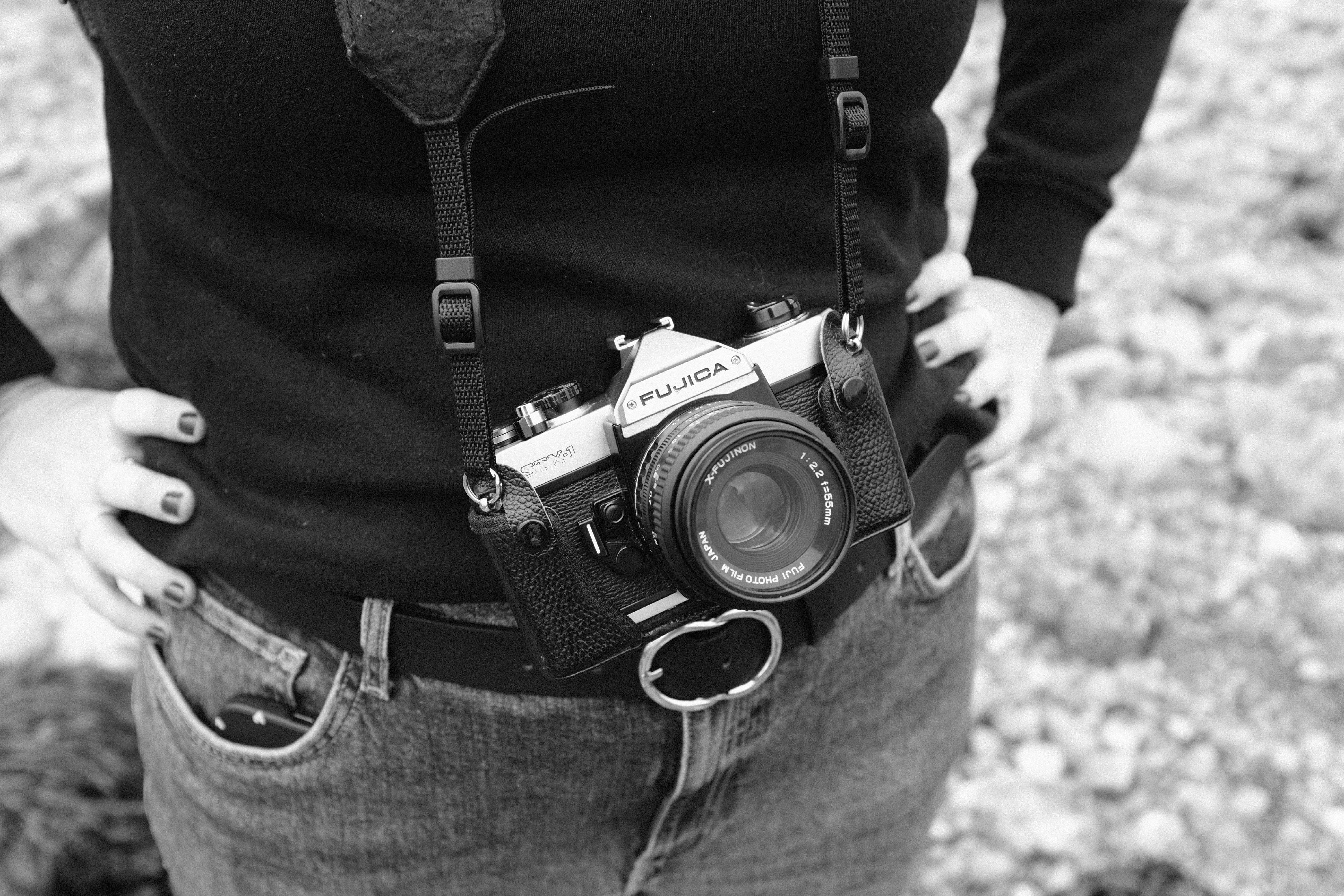 Vintage Fujica camera hangs from the waist of a person, set against a textured background of stones. The scene evokes nostalgia for classic photography.