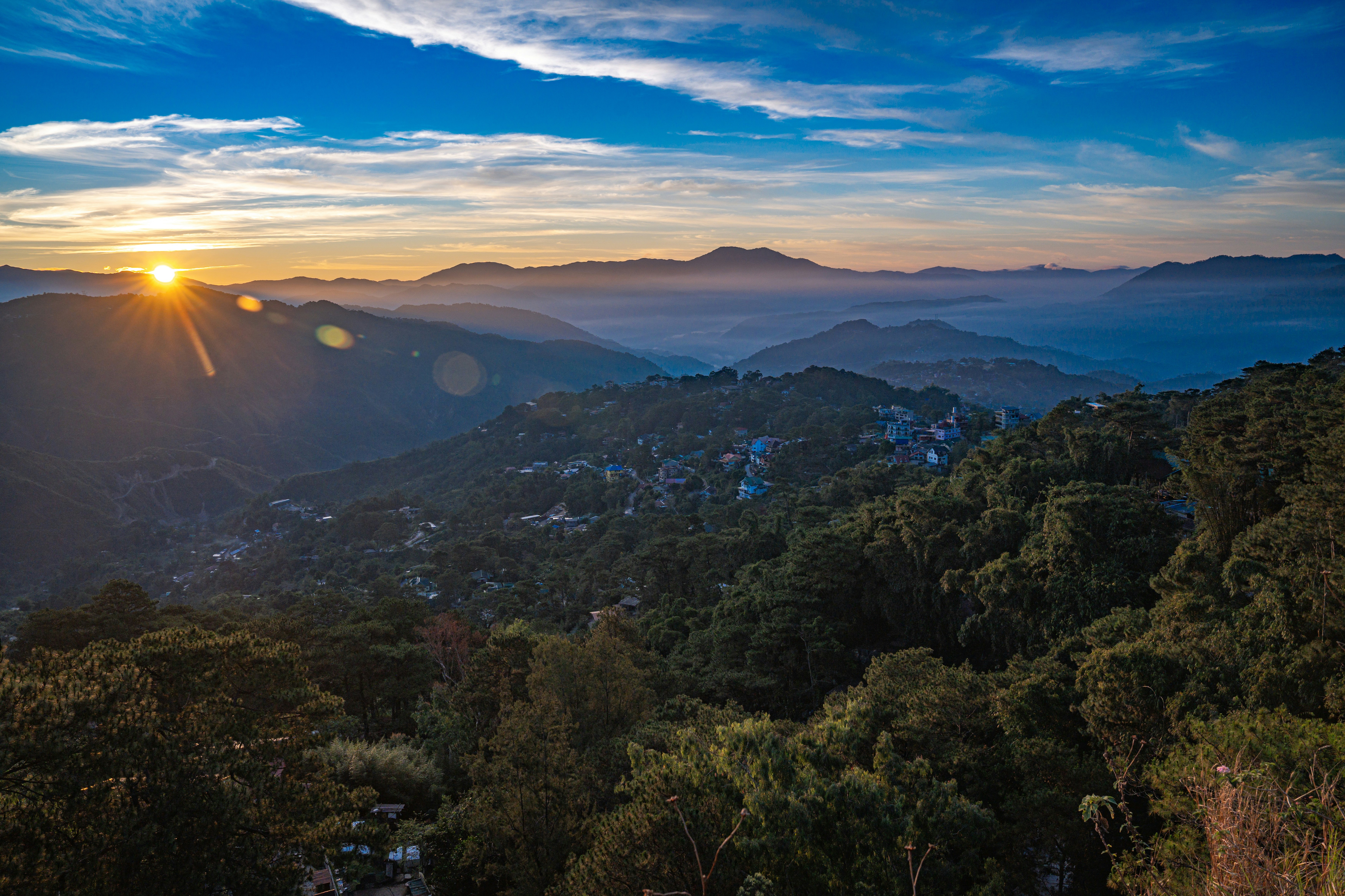 Sunrise over a misty mountain village with lush trees.