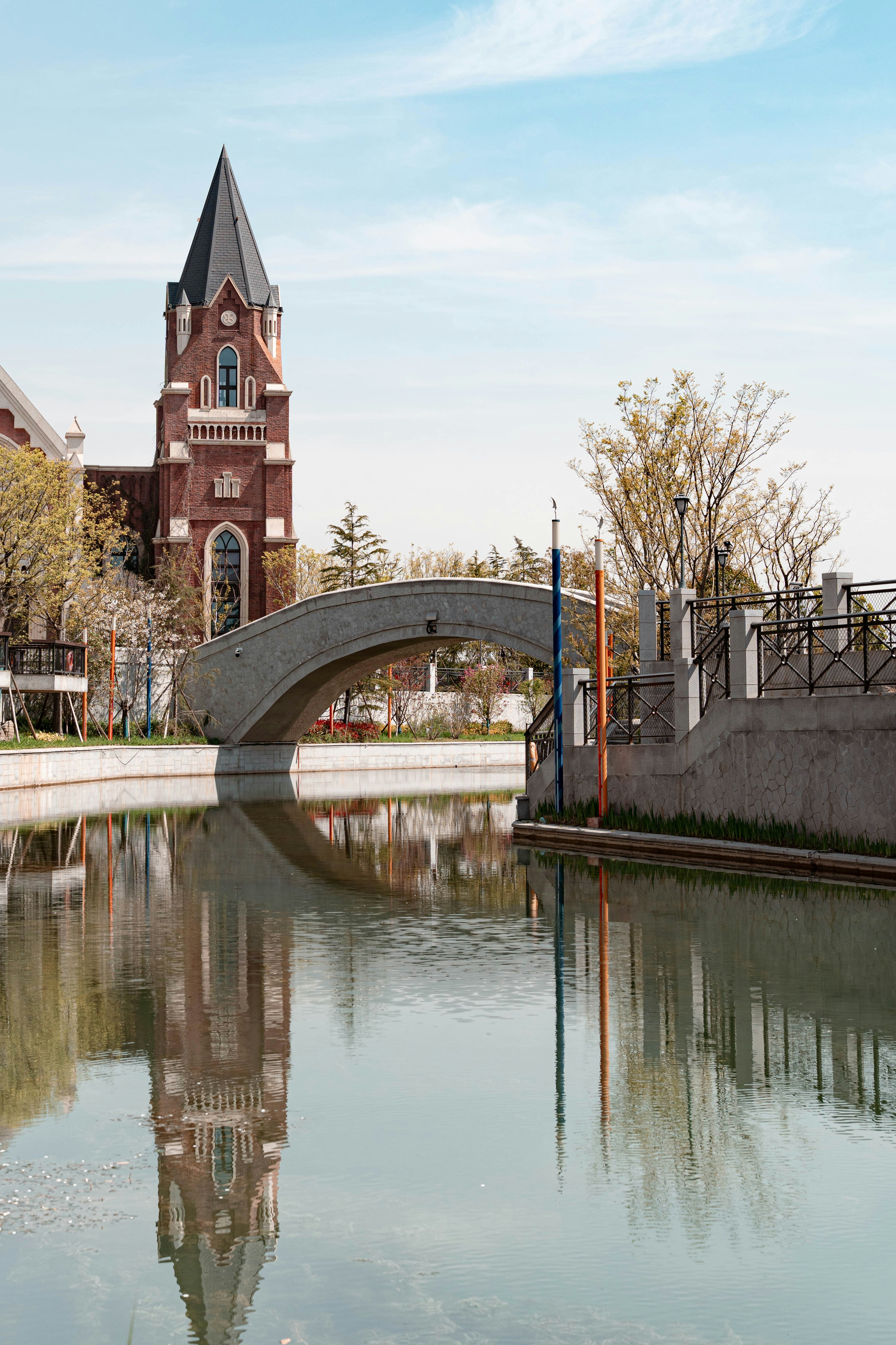 Historic building reflected in serene waters with a modern bridge arching over the canal. Trees frame the scene, enhancing the tranquil atmosphere.