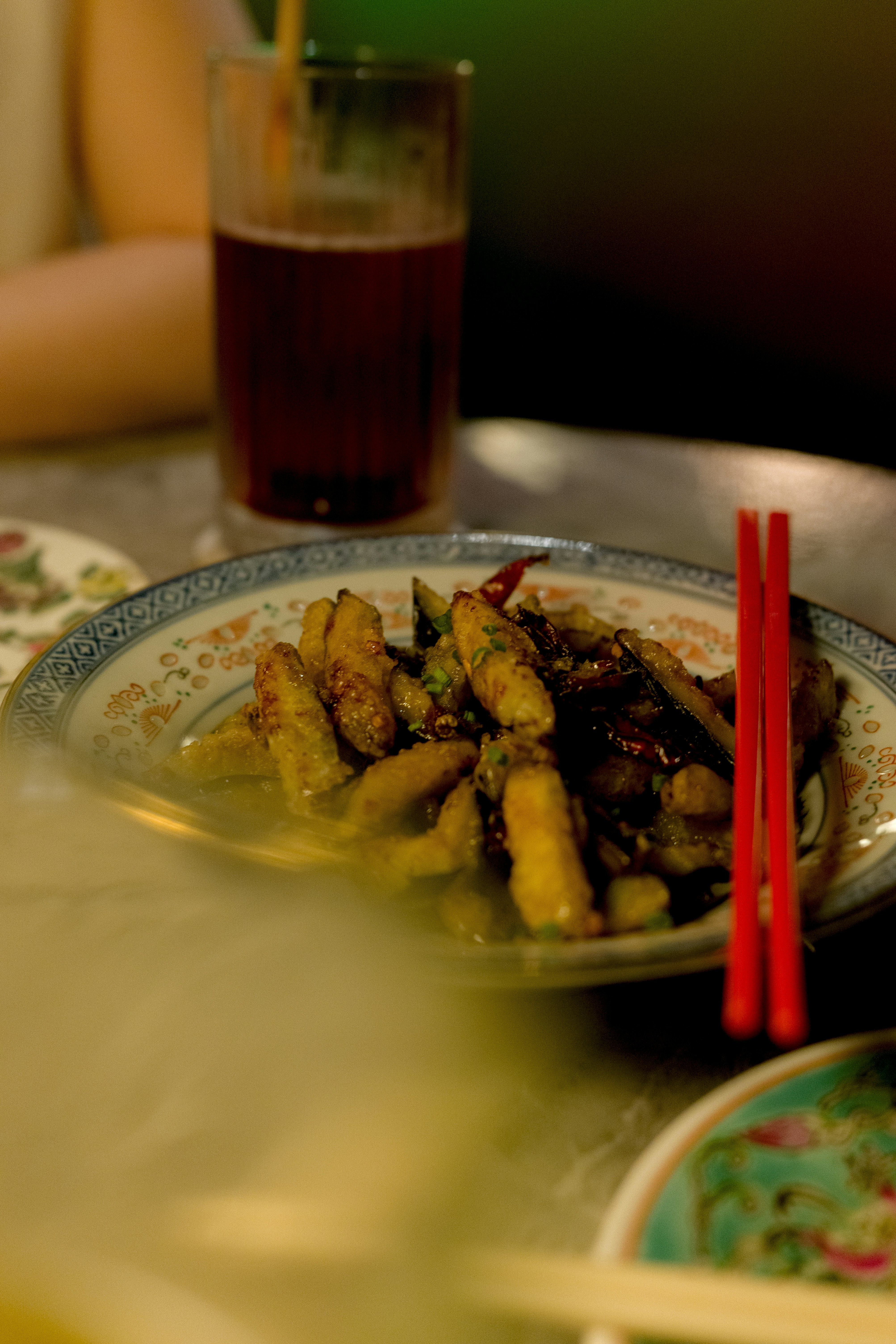 Plate of stir-fried vegetables and protein garnished with red chopsticks, set against a softly blurred background of a dining table. 