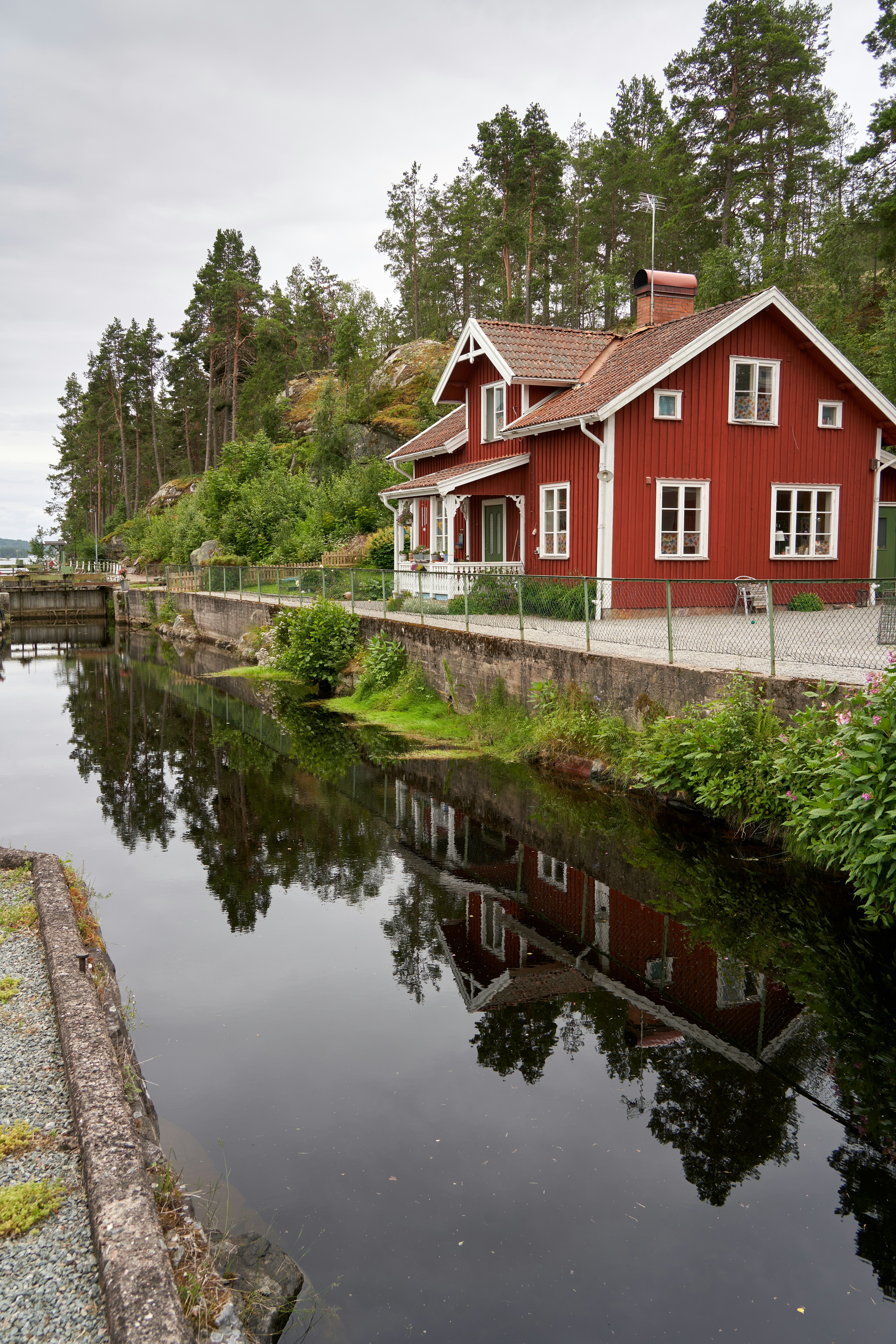 Traditiona scandinavian red wooden house by a lock on the Dalsland Canal, Sweden | Red house reflected in a calm canal with trees.