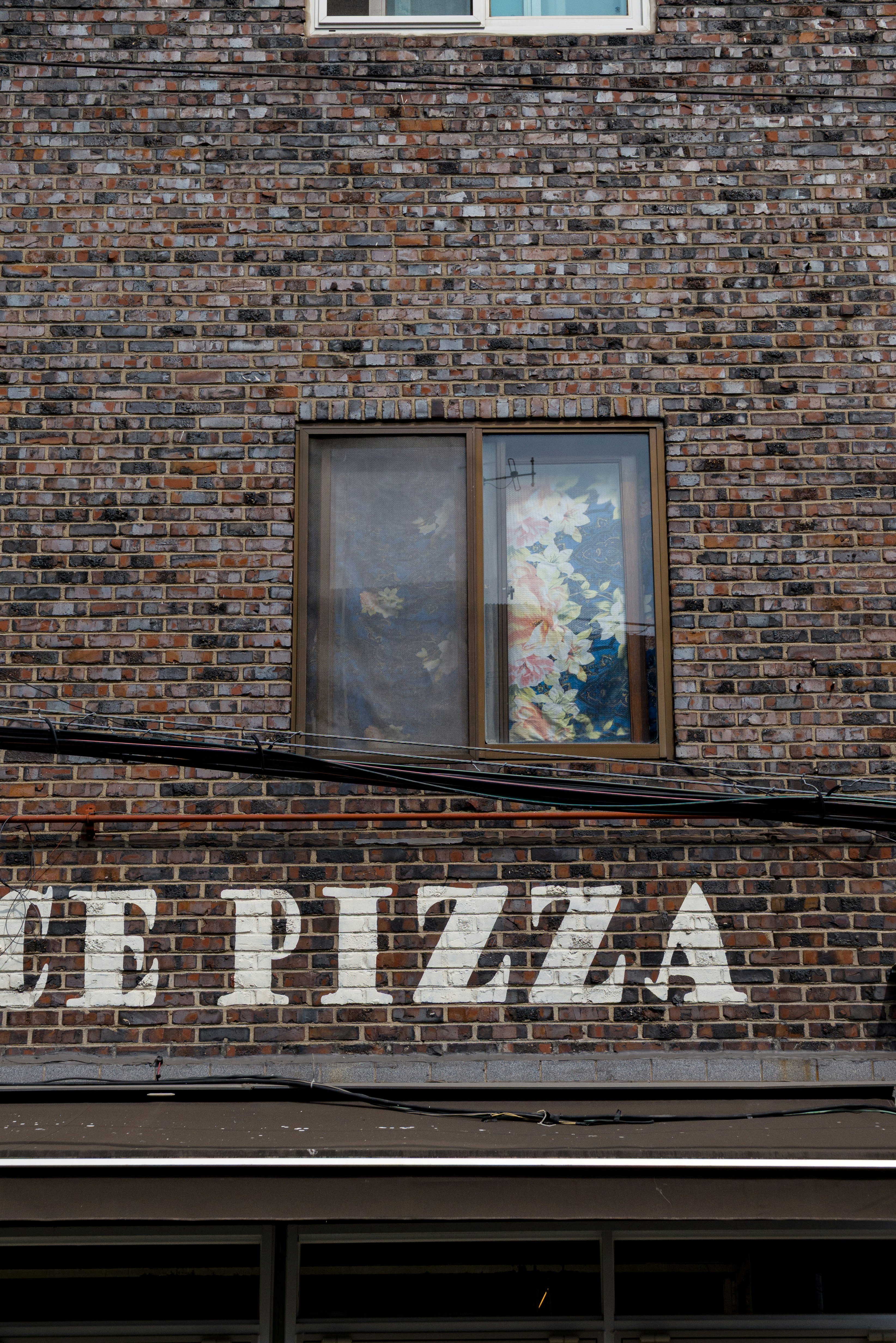 Flowers, Seoul | Brick wall with "pizza" sign and window.