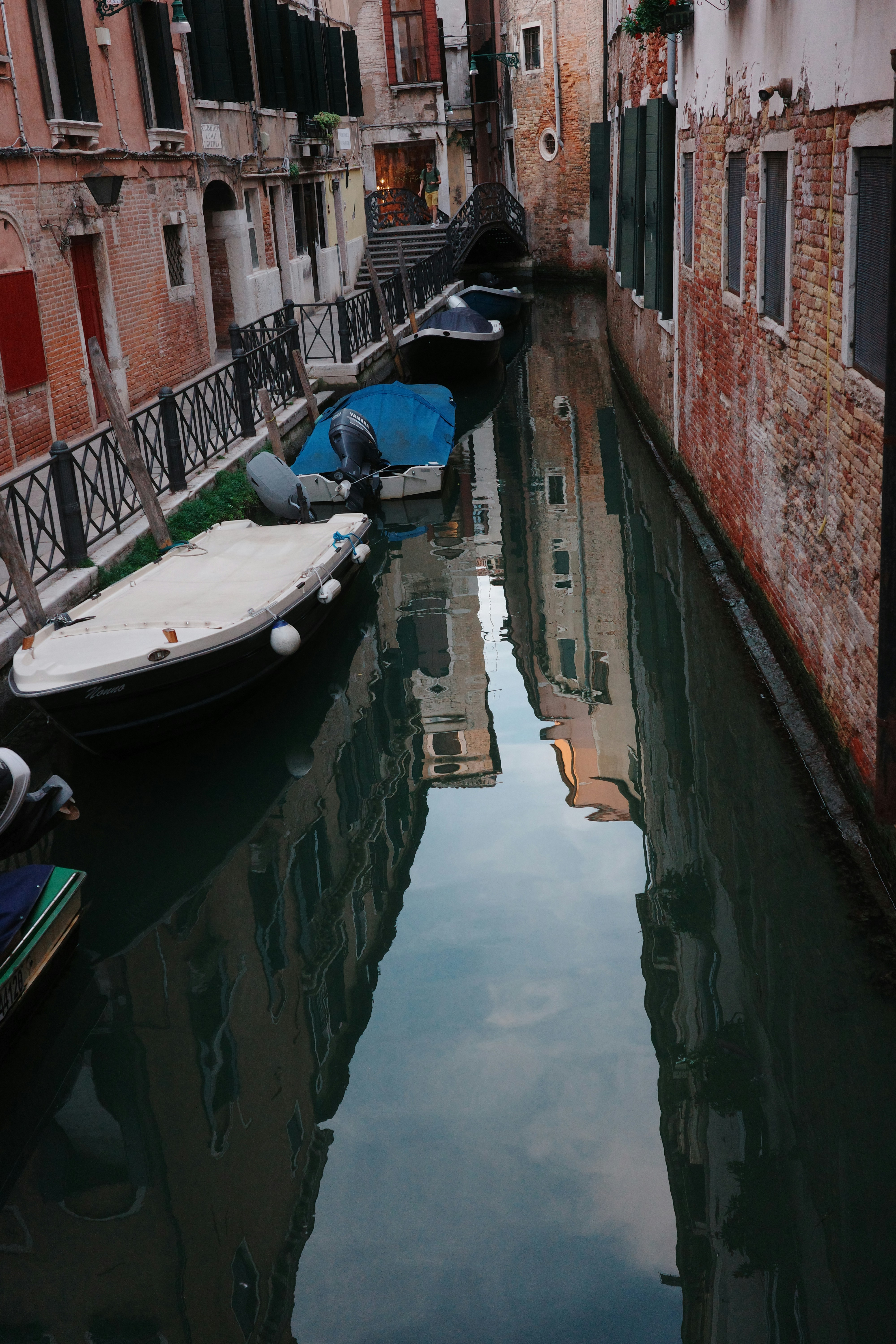 Quiet canal in Venice lined with rustic buildings and moored boats, reflecting the soft hues of the sky. A tranquil scene evoking the charm of Italian waterways.