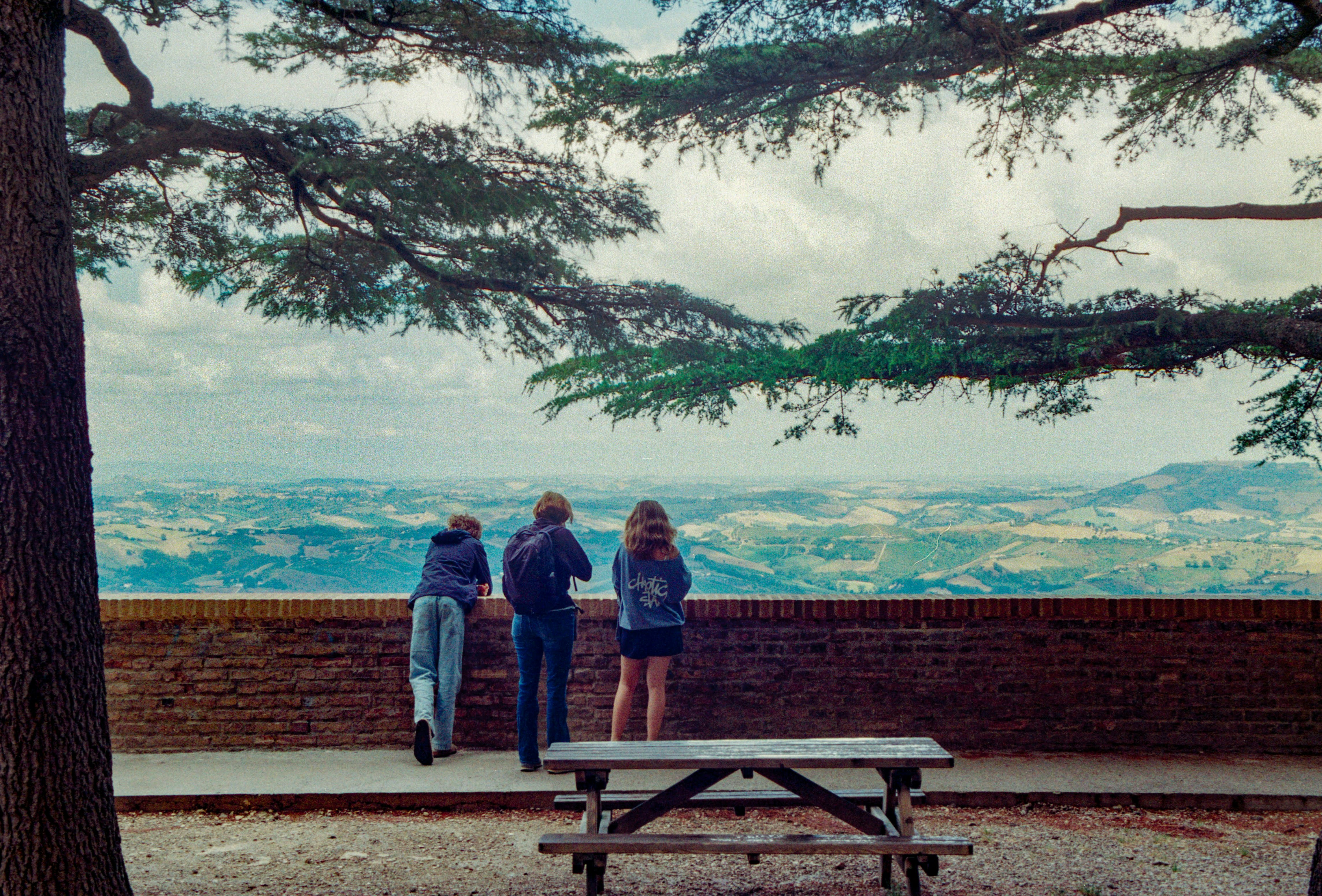 Three people admire a vast landscape from a viewpoint.