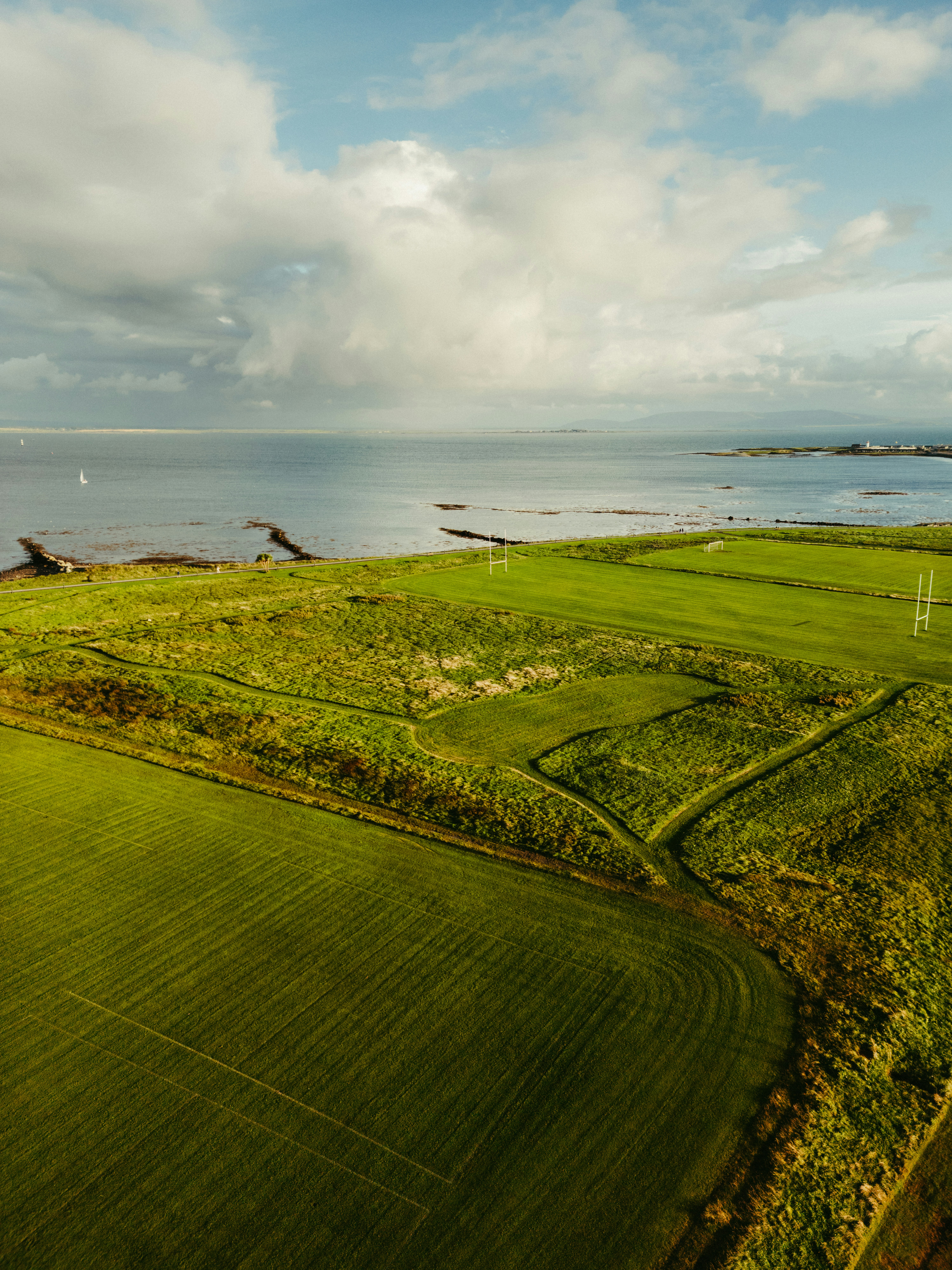 Lush green fields stretch toward the coastline, meeting the calm waters under a cloudy sky. The scene captures the harmony between land and sea.