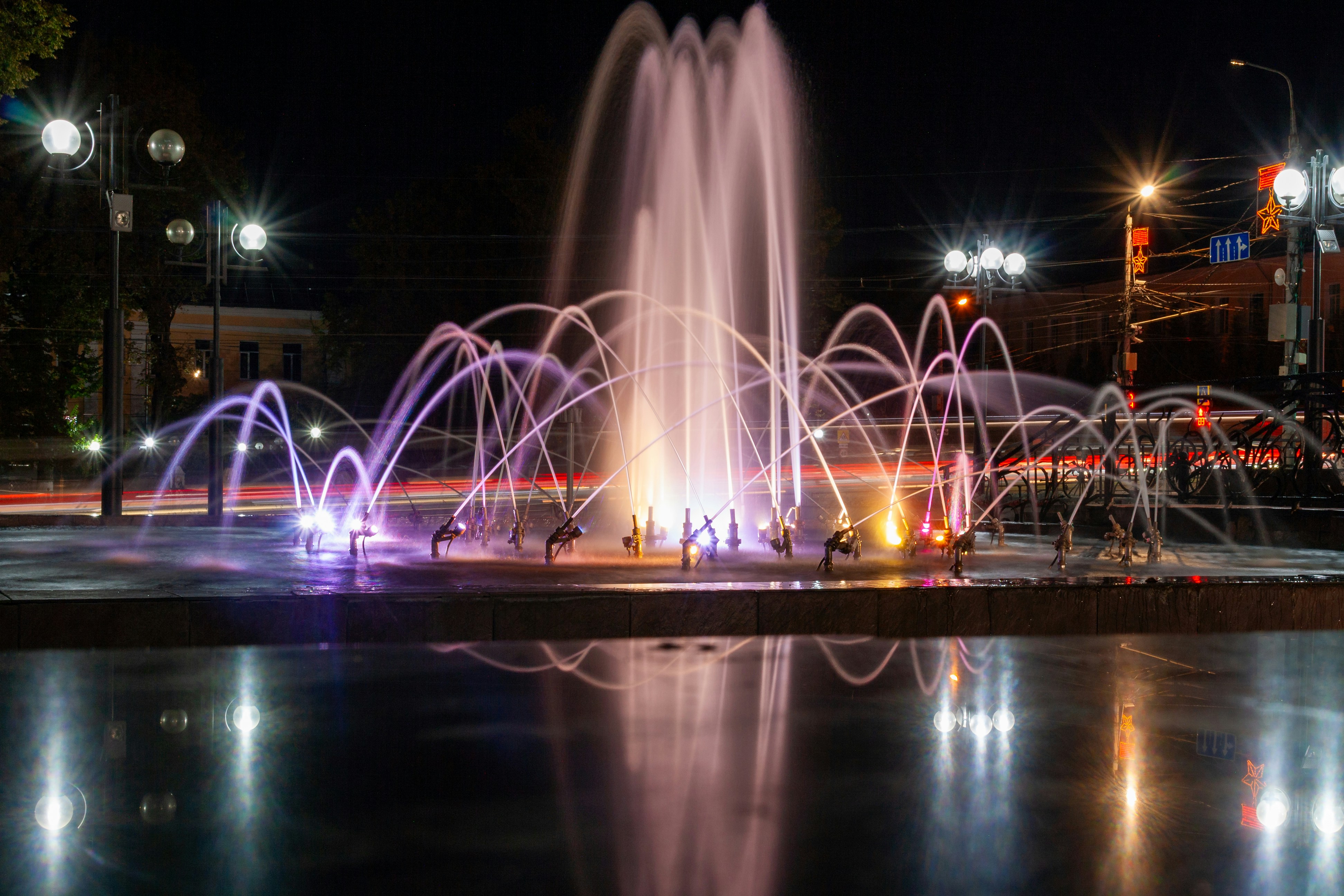 Illuminated fountain dancing with vibrant colors under the night sky, reflecting on a polished surface.