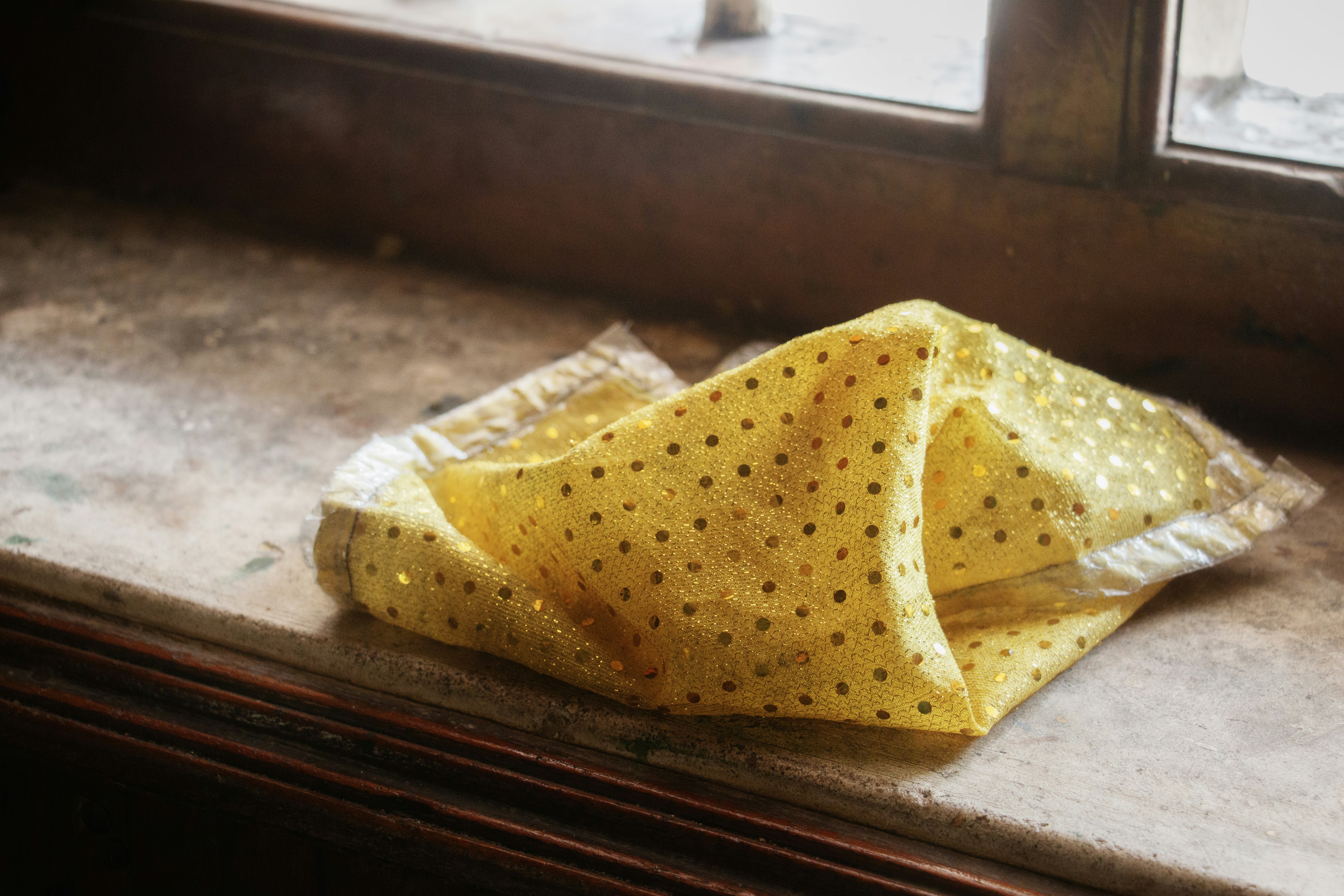 A crumpled yellow cloth with black polka dots on windowsill
