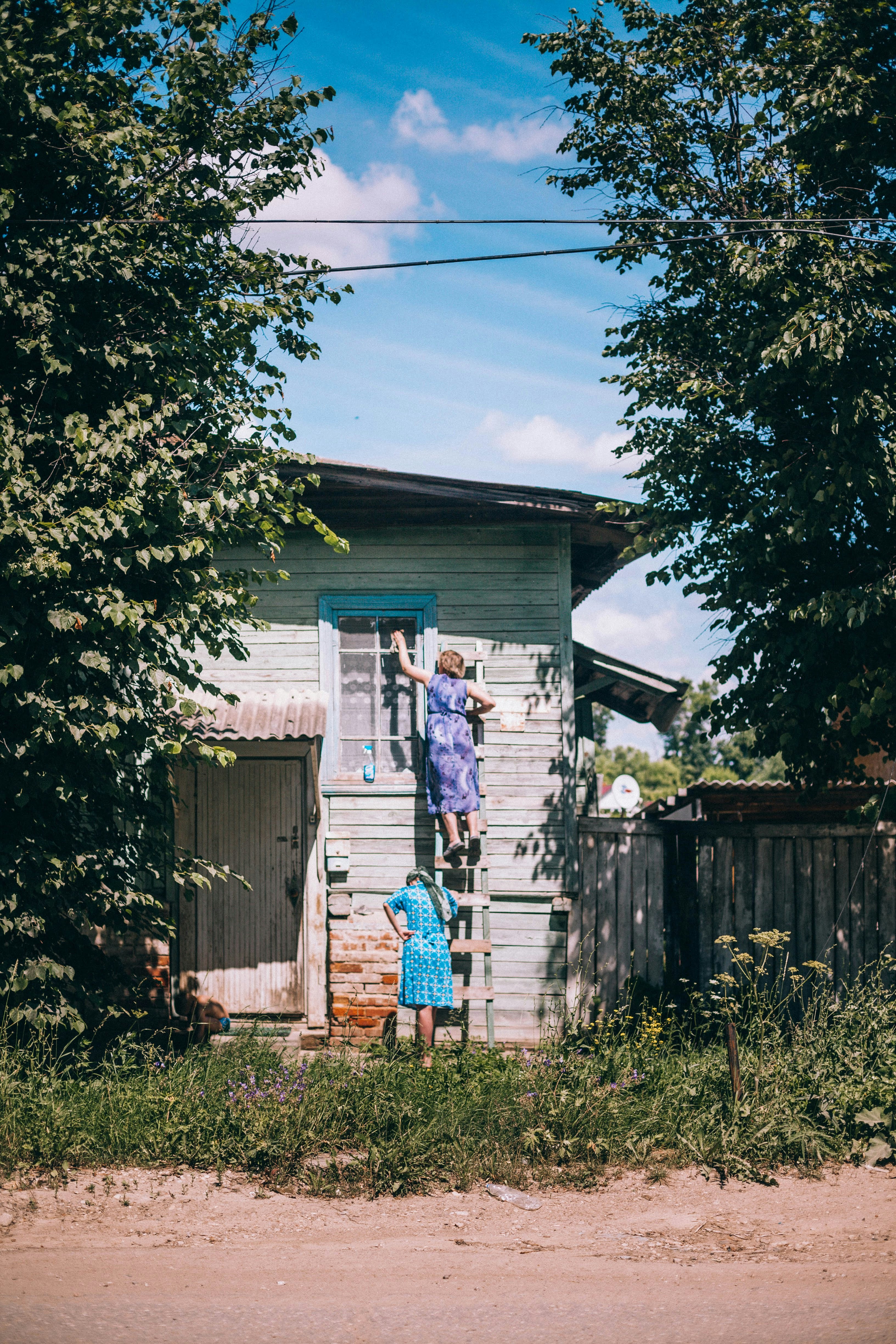 Two women washing a house exterior on a ladder.
