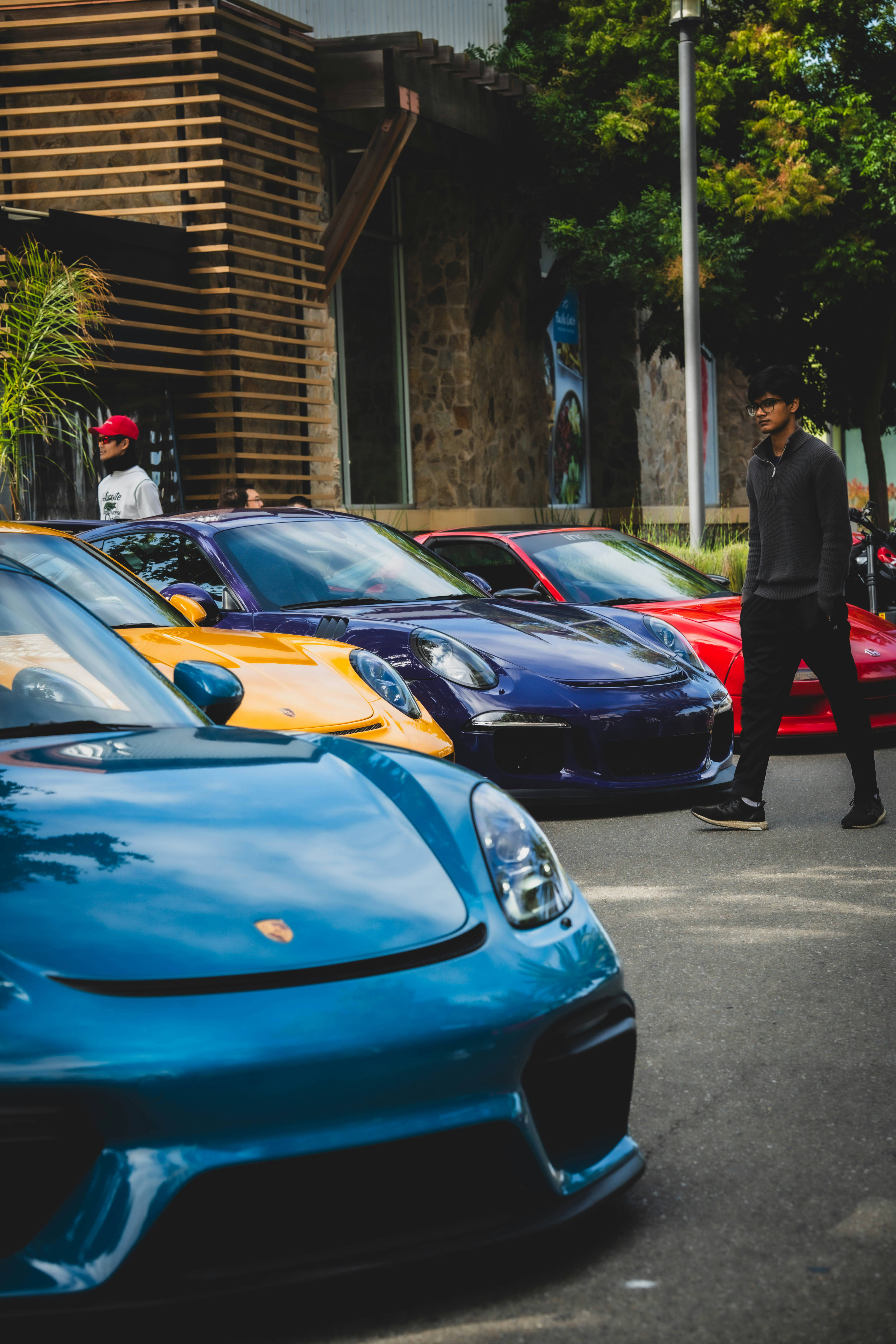 Chrome-Blue Lead: A tight street-side lineup of neon Porsches with a lone passerby