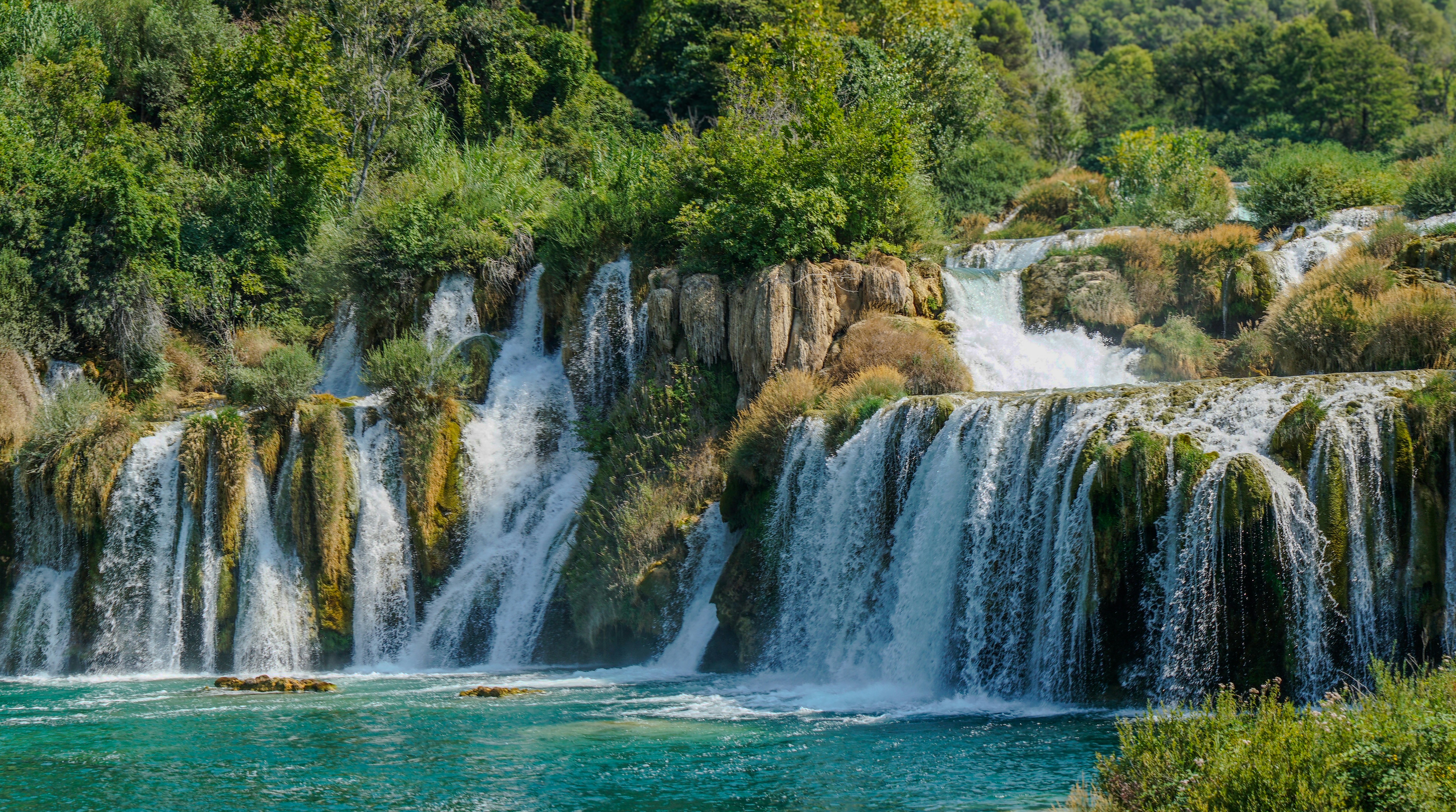 Cascading waterfalls flow into a turquoise pool surrounded by greenery.