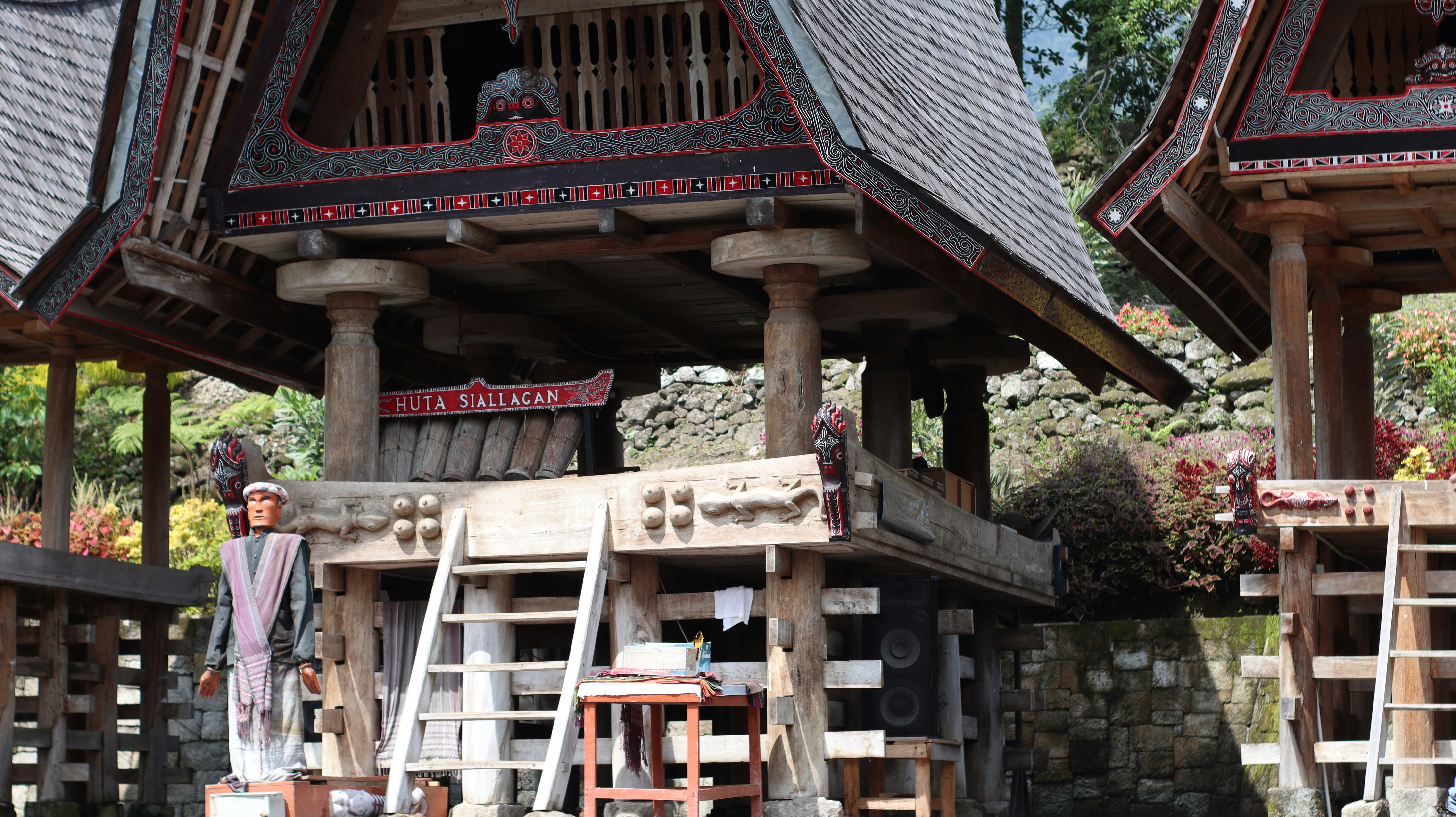 Traditional Batak houses showcasing unique architecture in Huta Siallagan, with a figure dressed in cultural attire nearby.