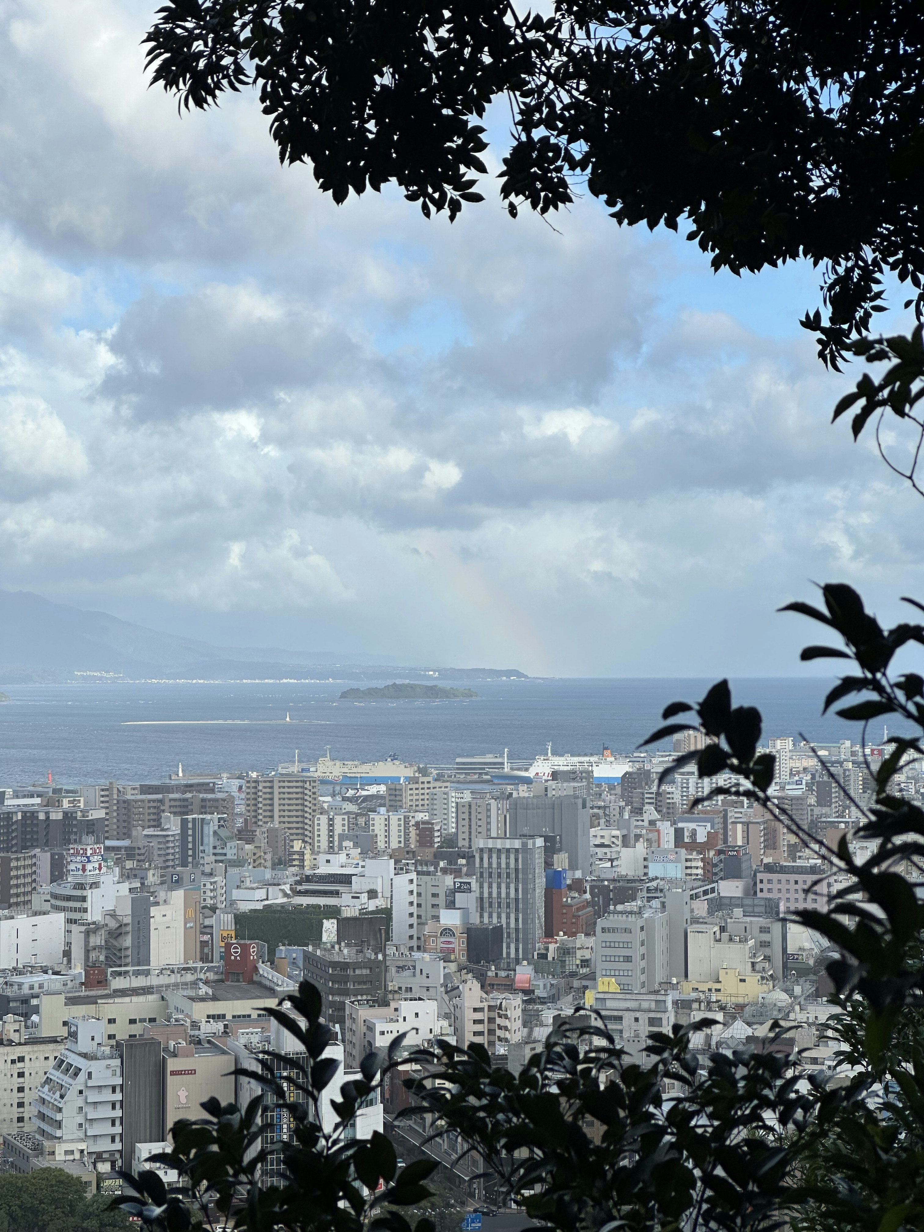 Cityscape with distant island and rainbow over ocean.