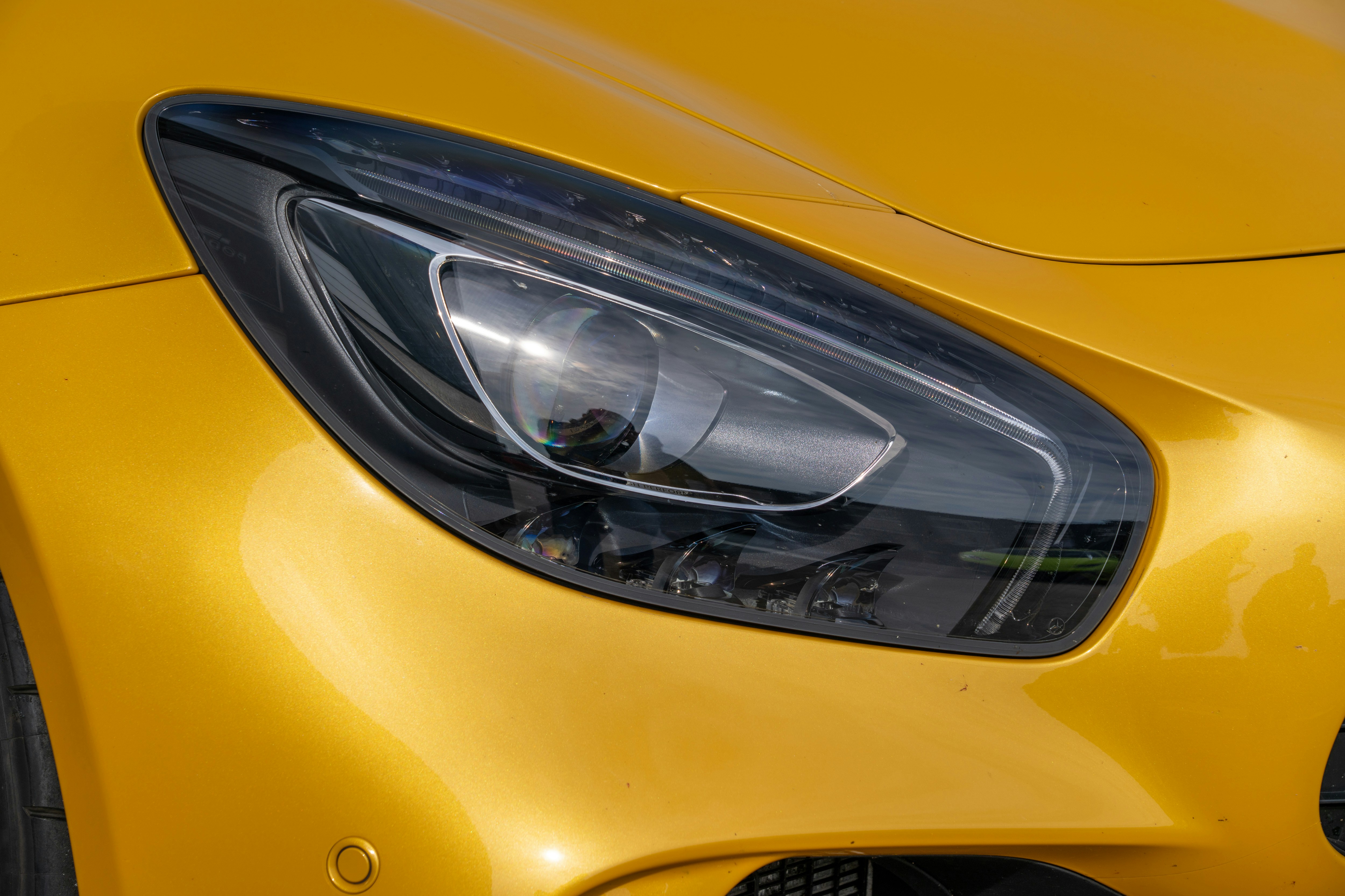 Close-up of a sleek car headlight showcasing intricate design and vibrant yellow paint finish.