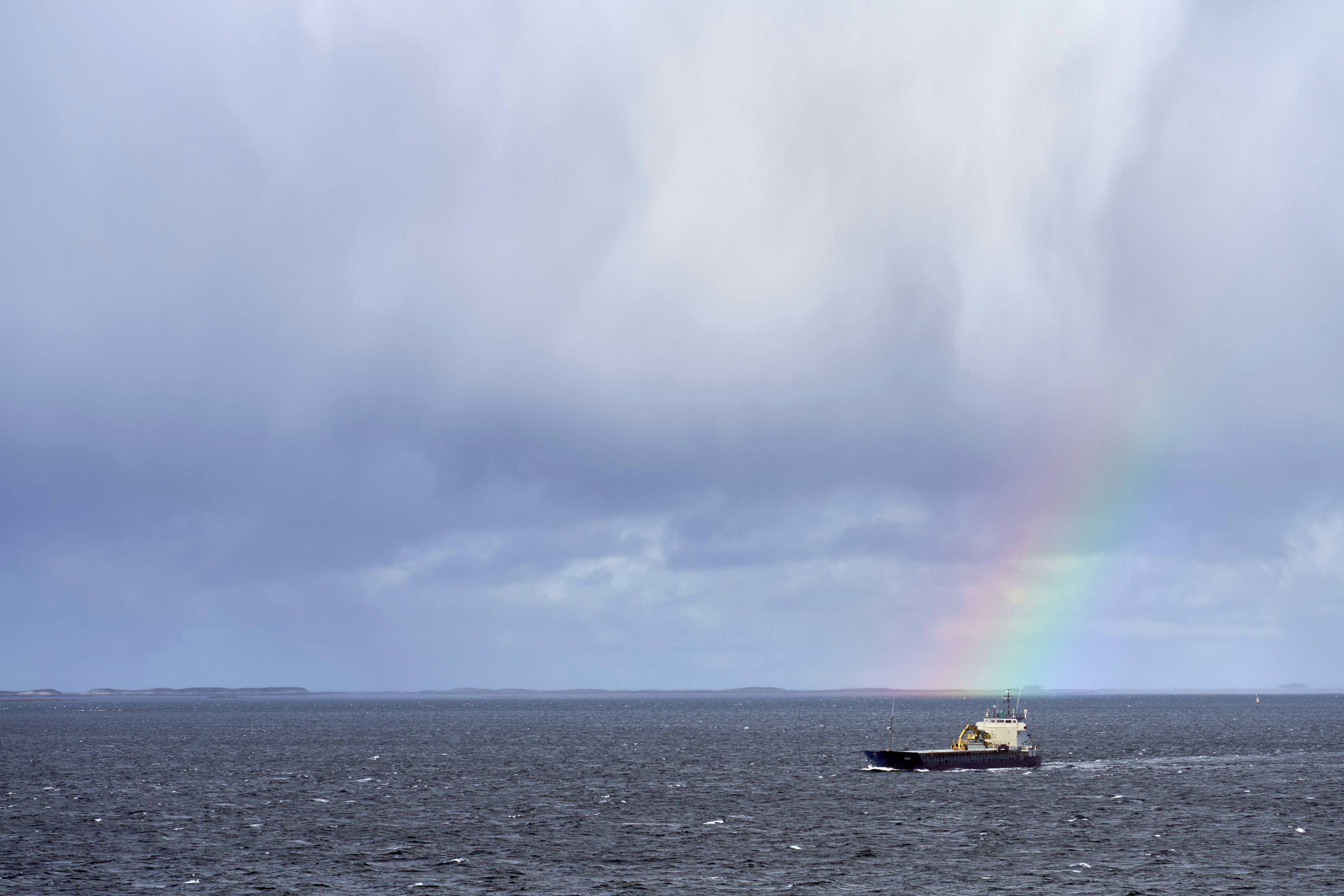 A tugboat sails through choppy seas under a rainbow.