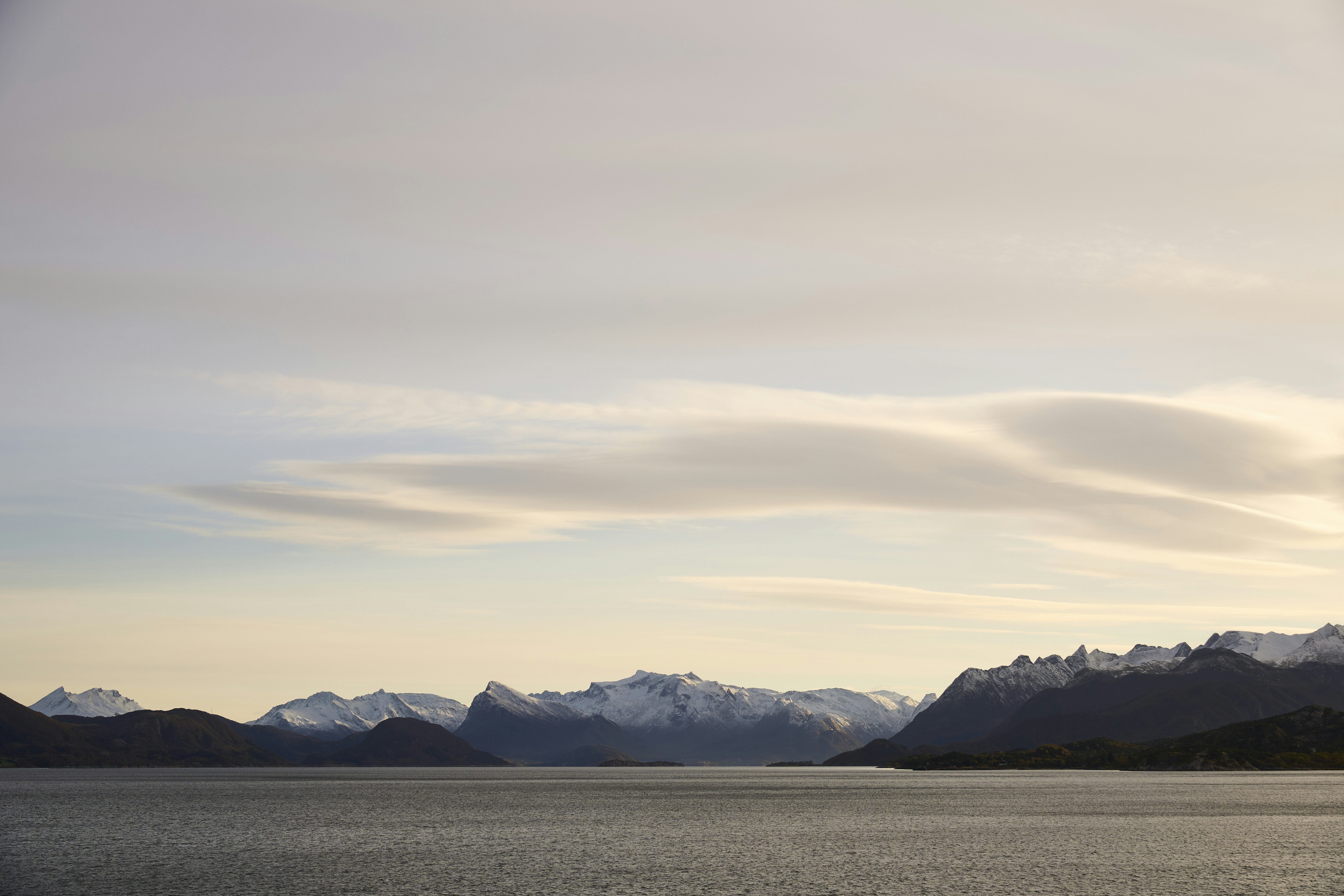 A tranquil seascape featuring distant snow-capped mountains under a softly lit sky, with gentle waves reflecting the serene atmosphere.